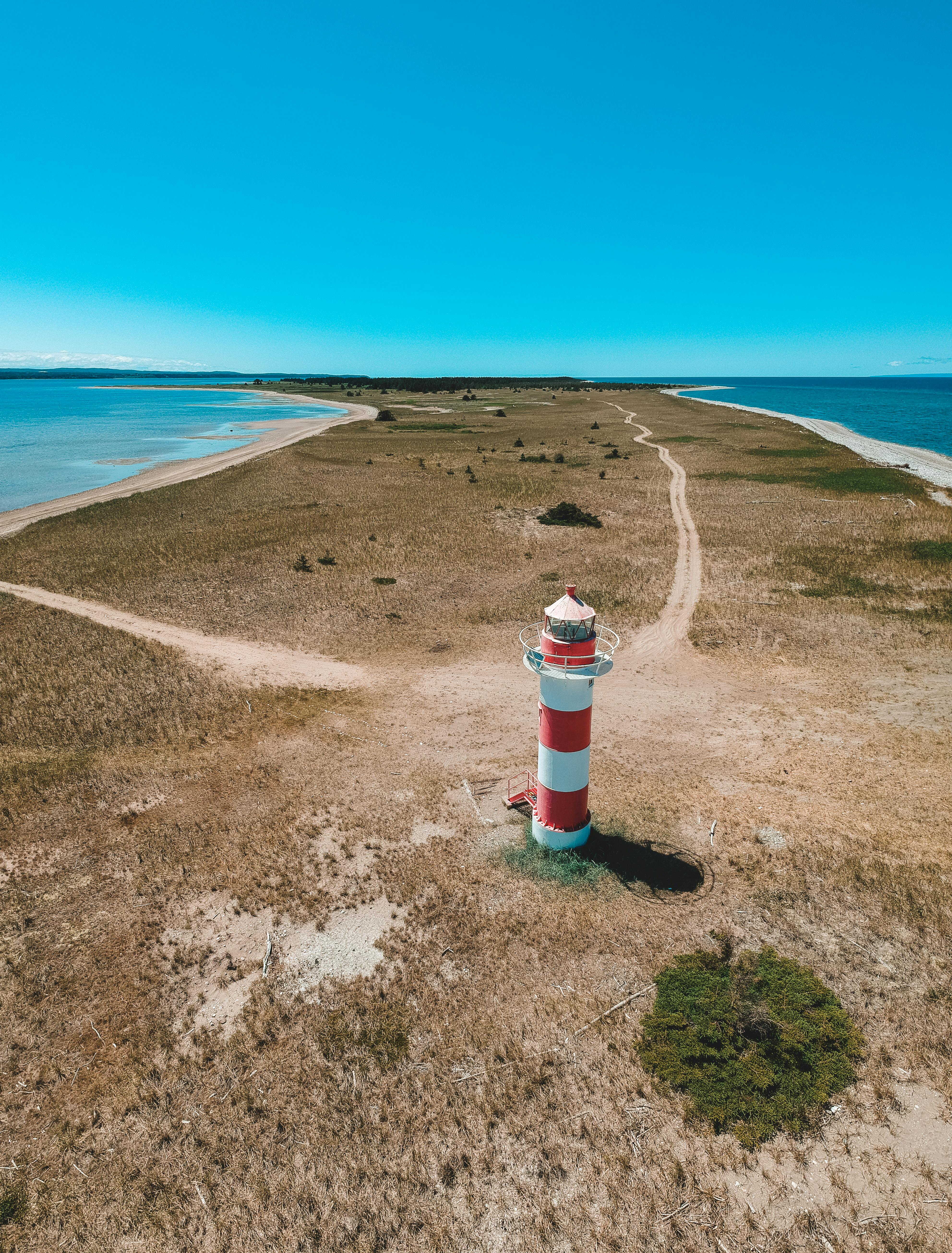 Bright lighthouse on island between sea under blue sky · Free Stock Photo