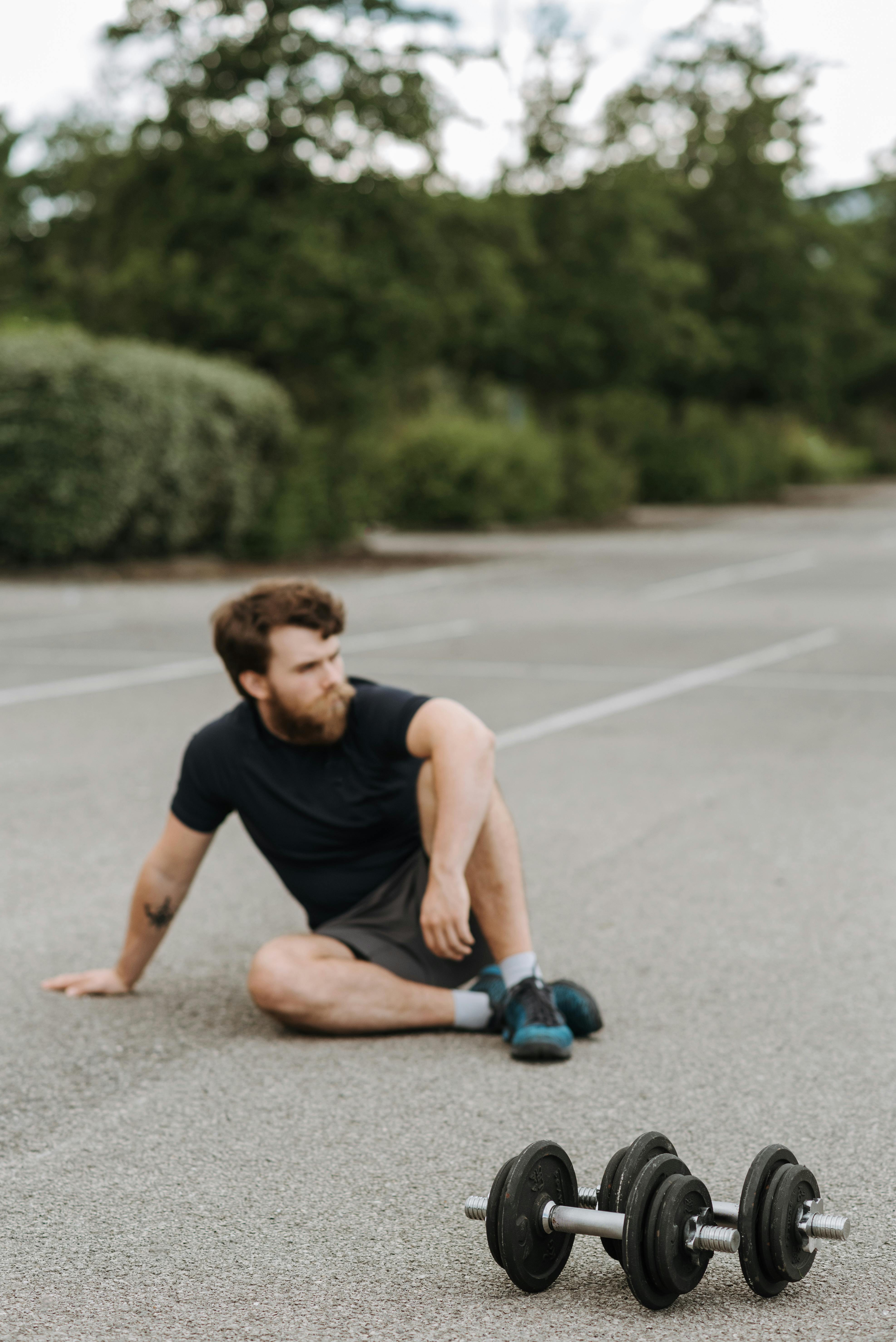 Young strong man resting on asphalt road with dumbbells · Free Stock Photo