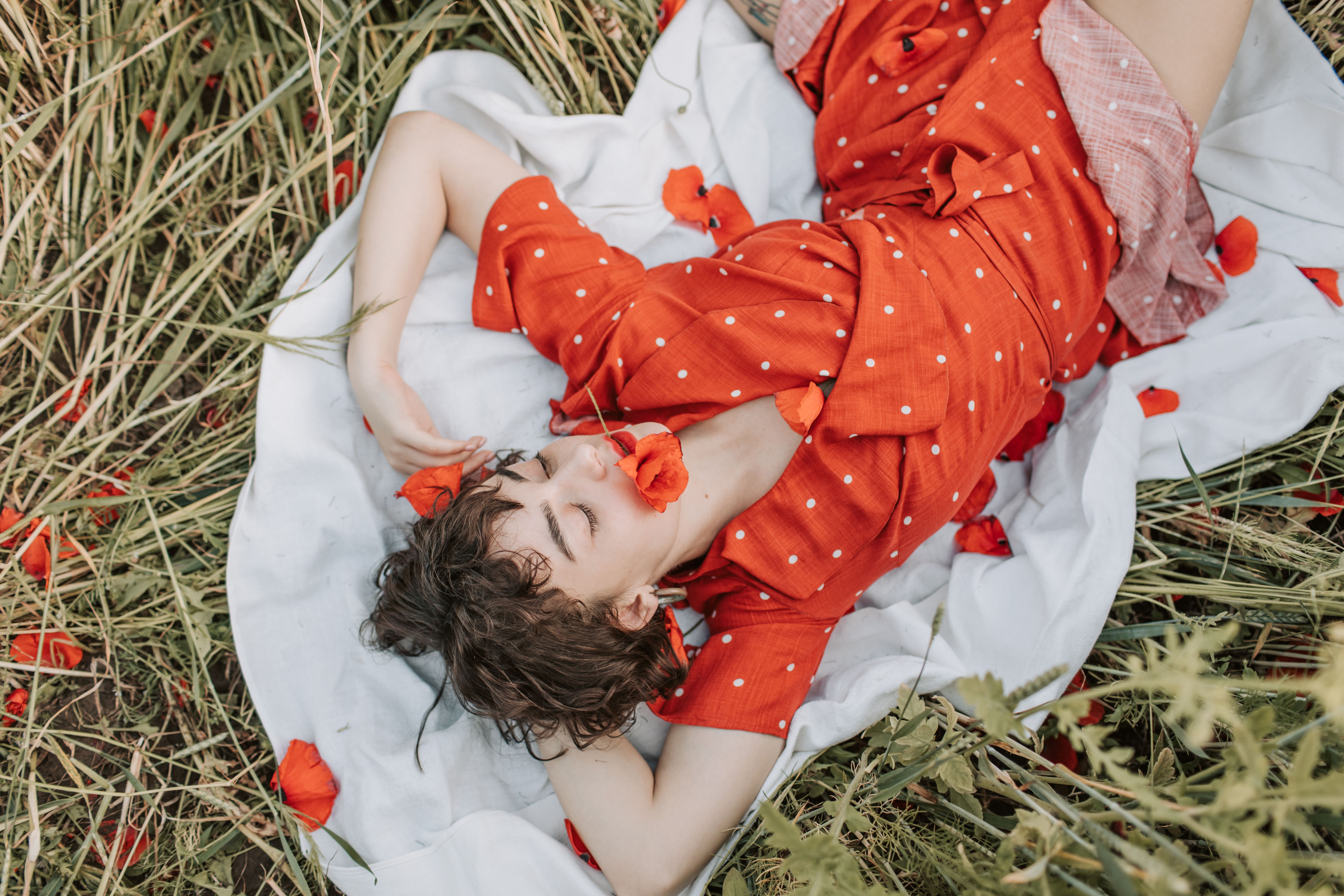 A Woman Biting a Poppy Flower While Lying Down · Free Stock Photo