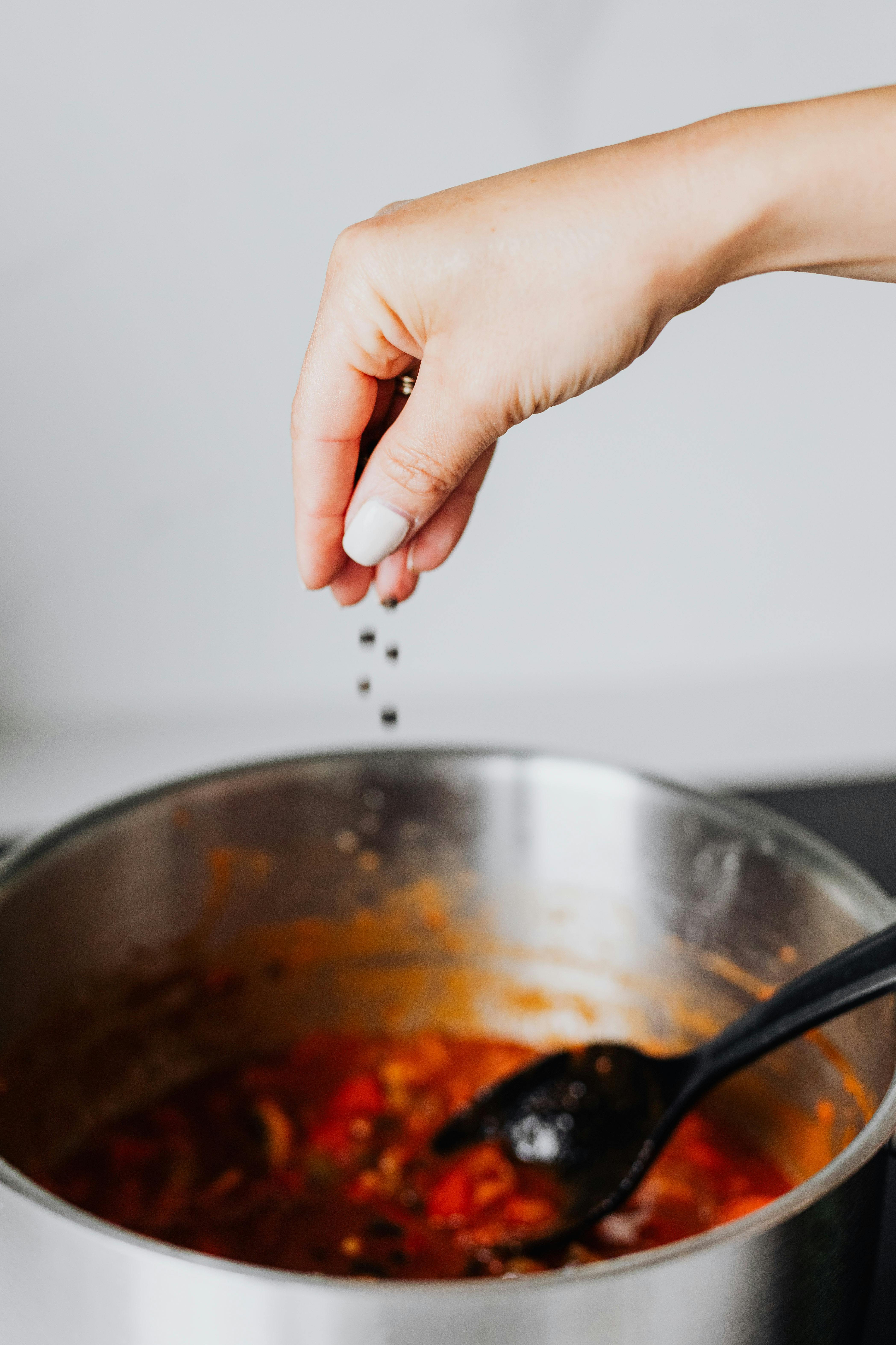 Photo of a Person Putting Black Pepper into a Pot · Free Stock Photo