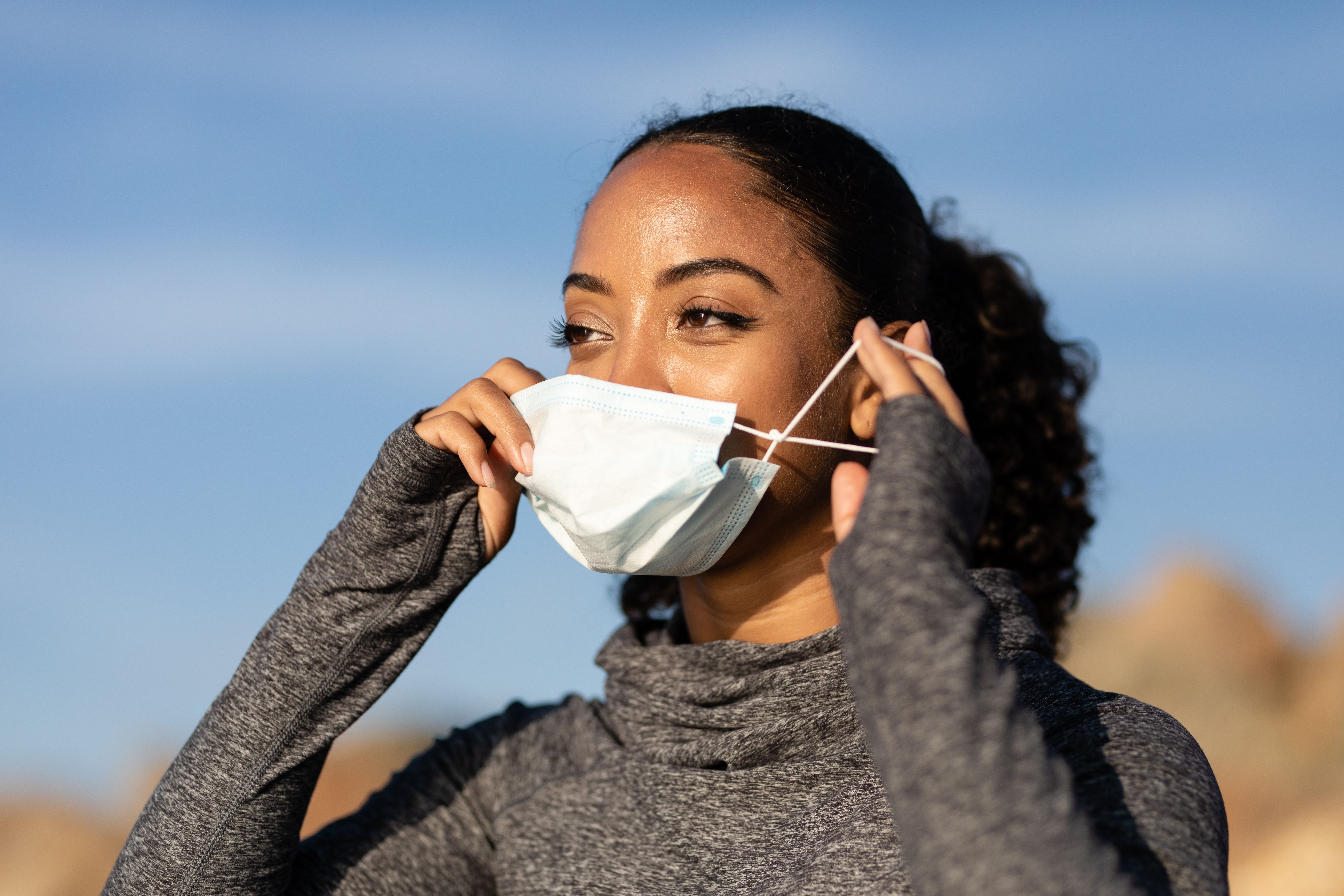 Woman in Gray Sweater Putting on White Face Mask · Free Stock Photo