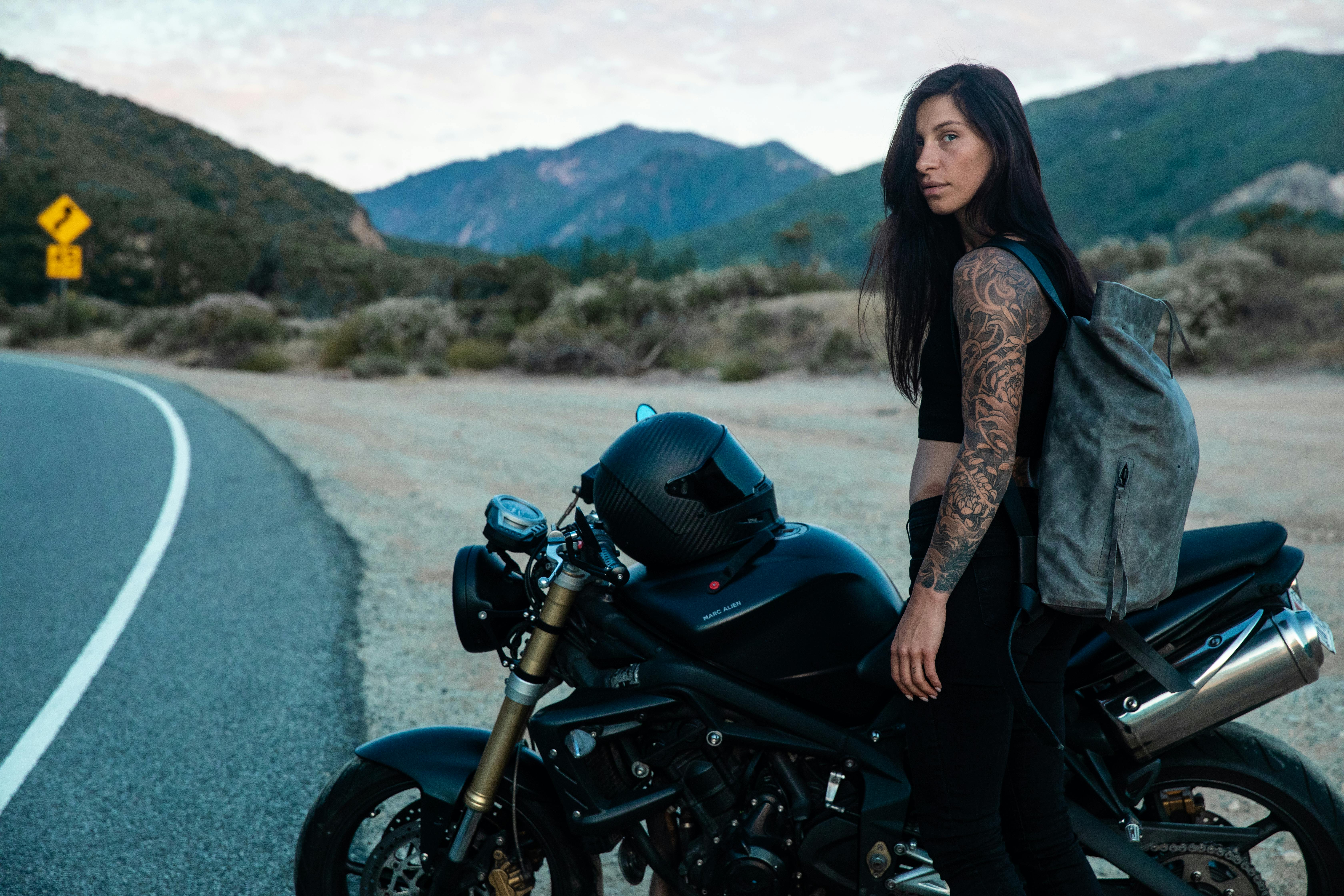 Tattooed Woman with Backpack Standing Beside a Black Motorcycle by the ...
