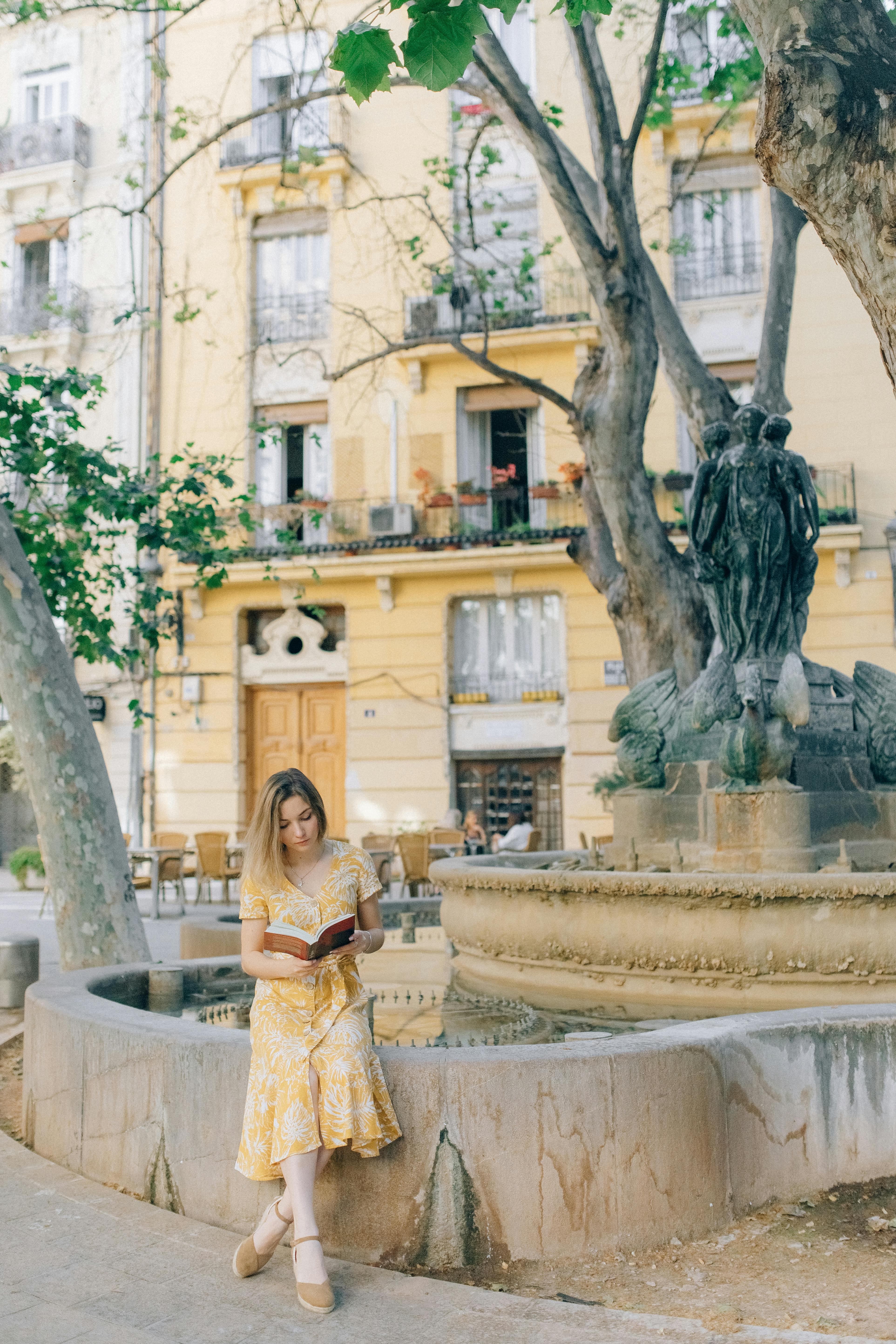 Woman in Yellow Dress Sitting on Fountain while Reading a Book · Free ...