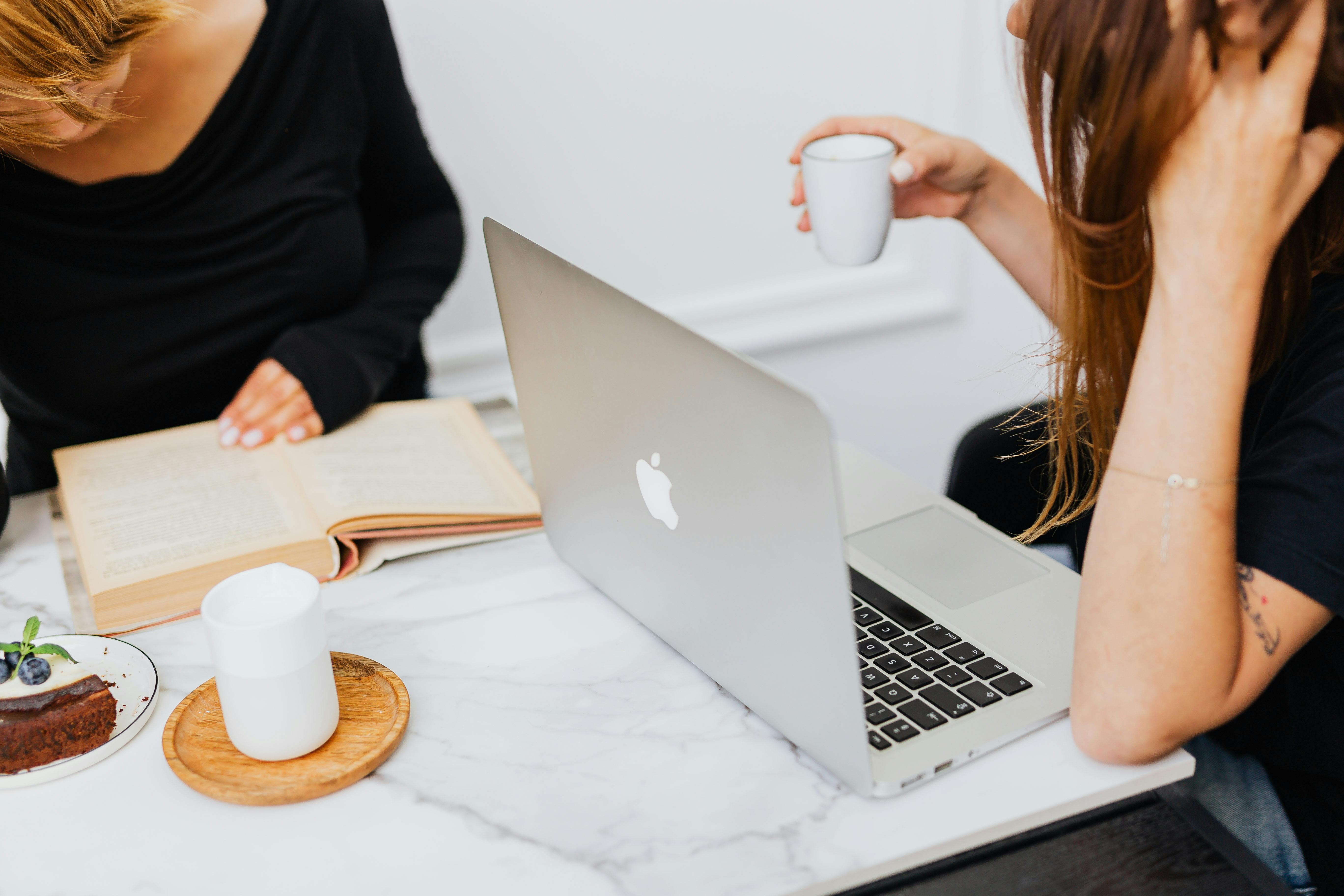 Women Using a Laptop and Reading a Book · Free Stock Photo