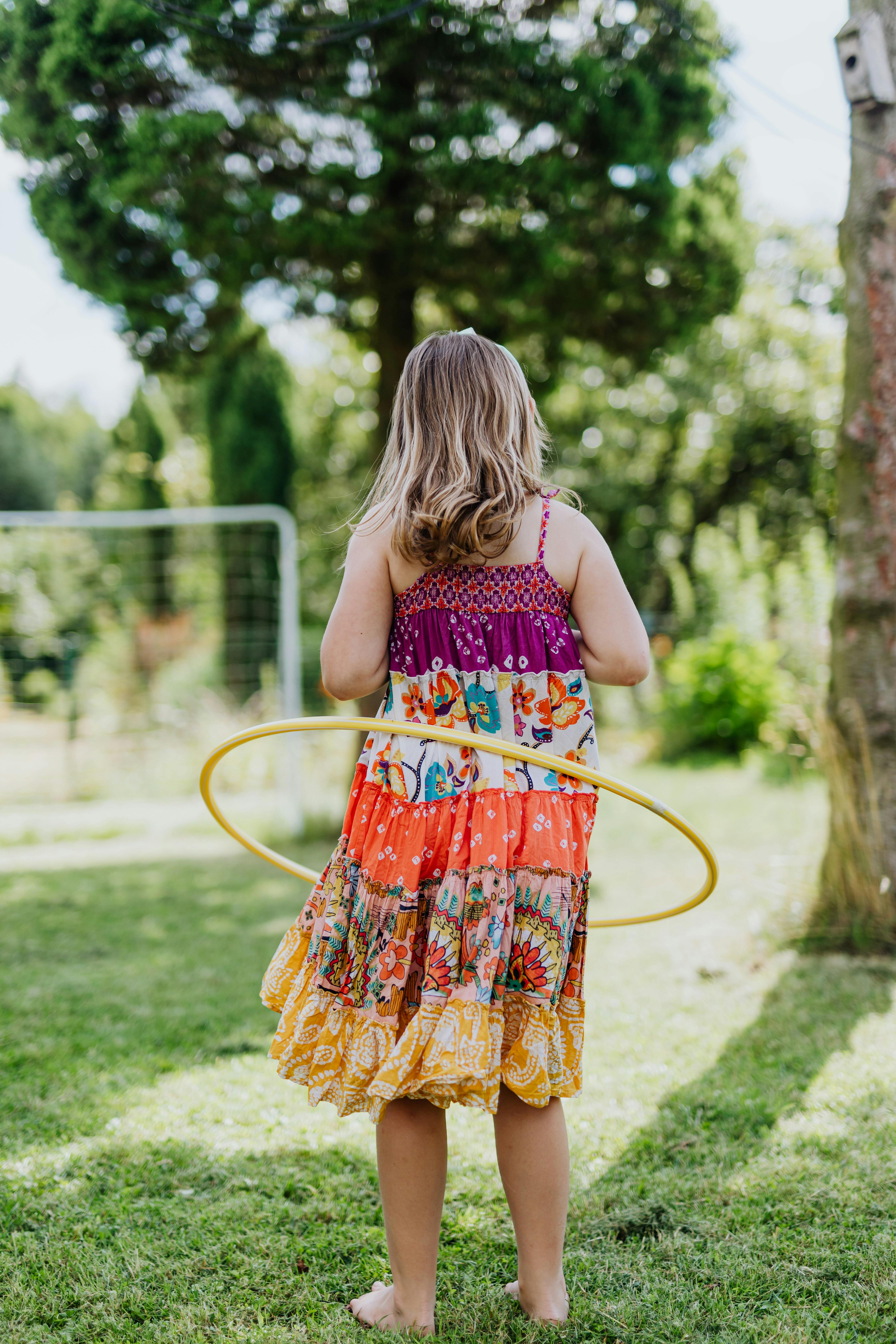 A Girl in Floral Dress Standing on the Green Grass While Doing Hula ...