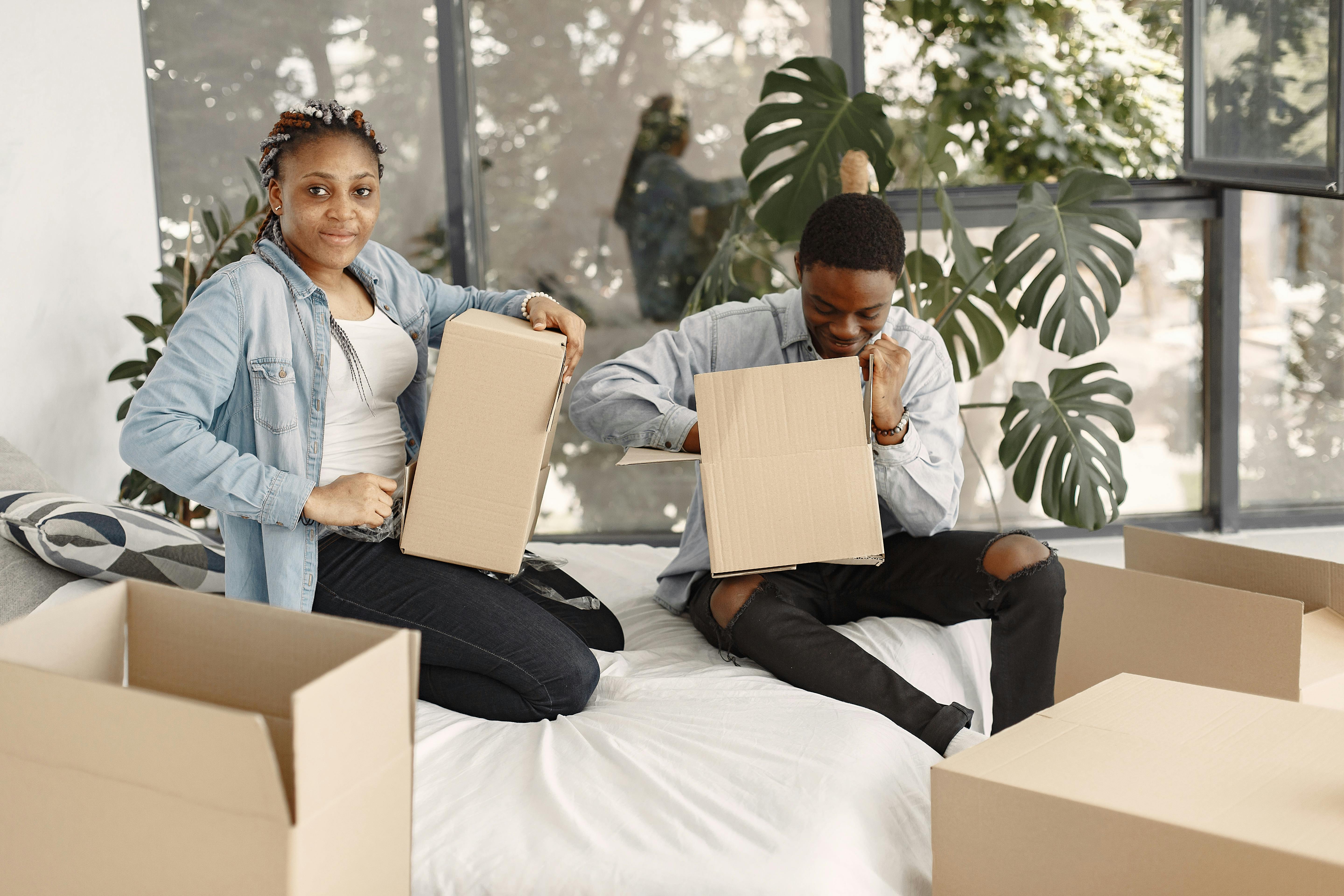 A Young Couple Holding Cardboard Boxes while Sitting on a Bed · Free ...