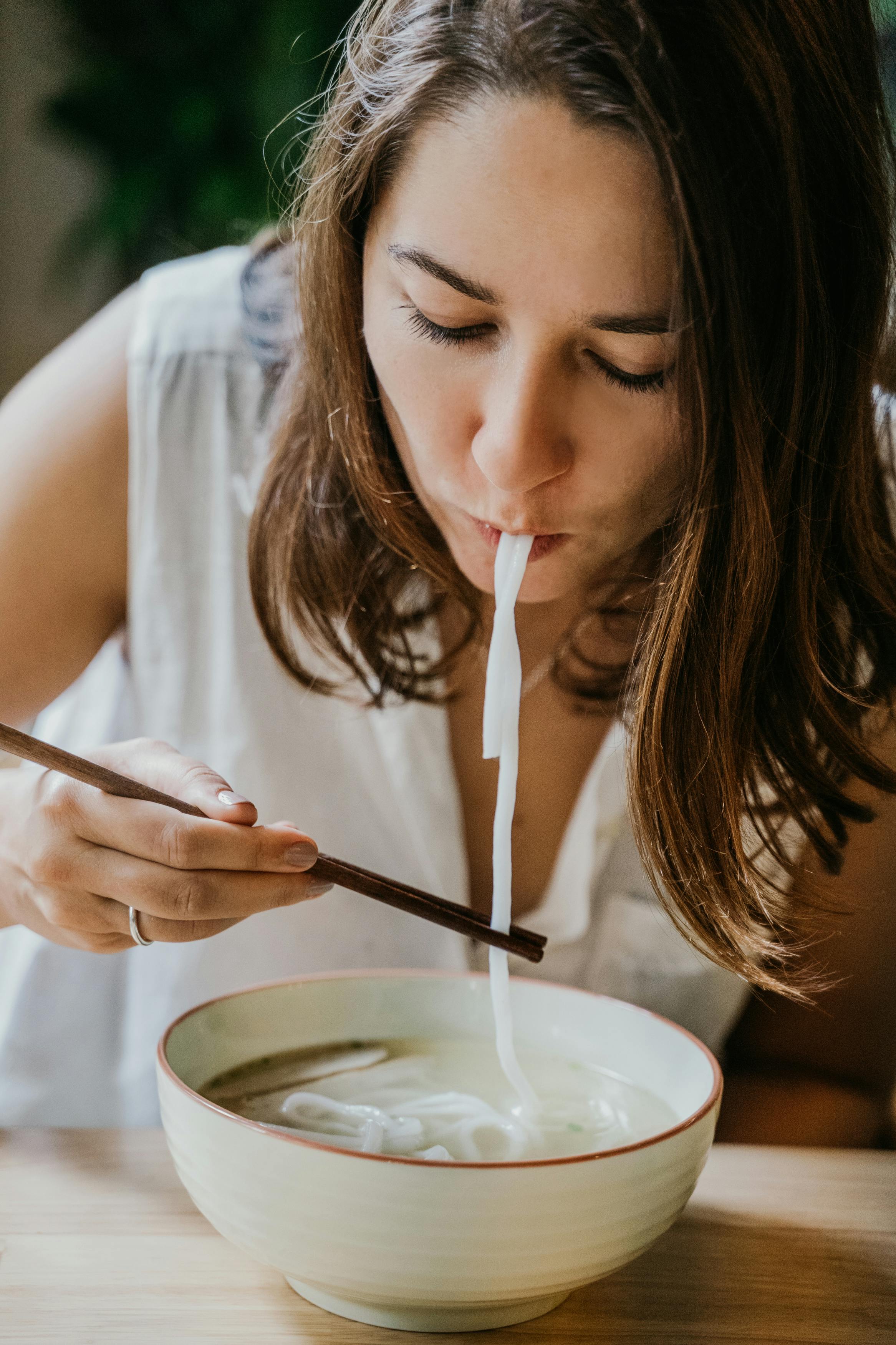 Woman in a White Dress Shirt Using Chopsticks to Eat Noodles · Free ...
