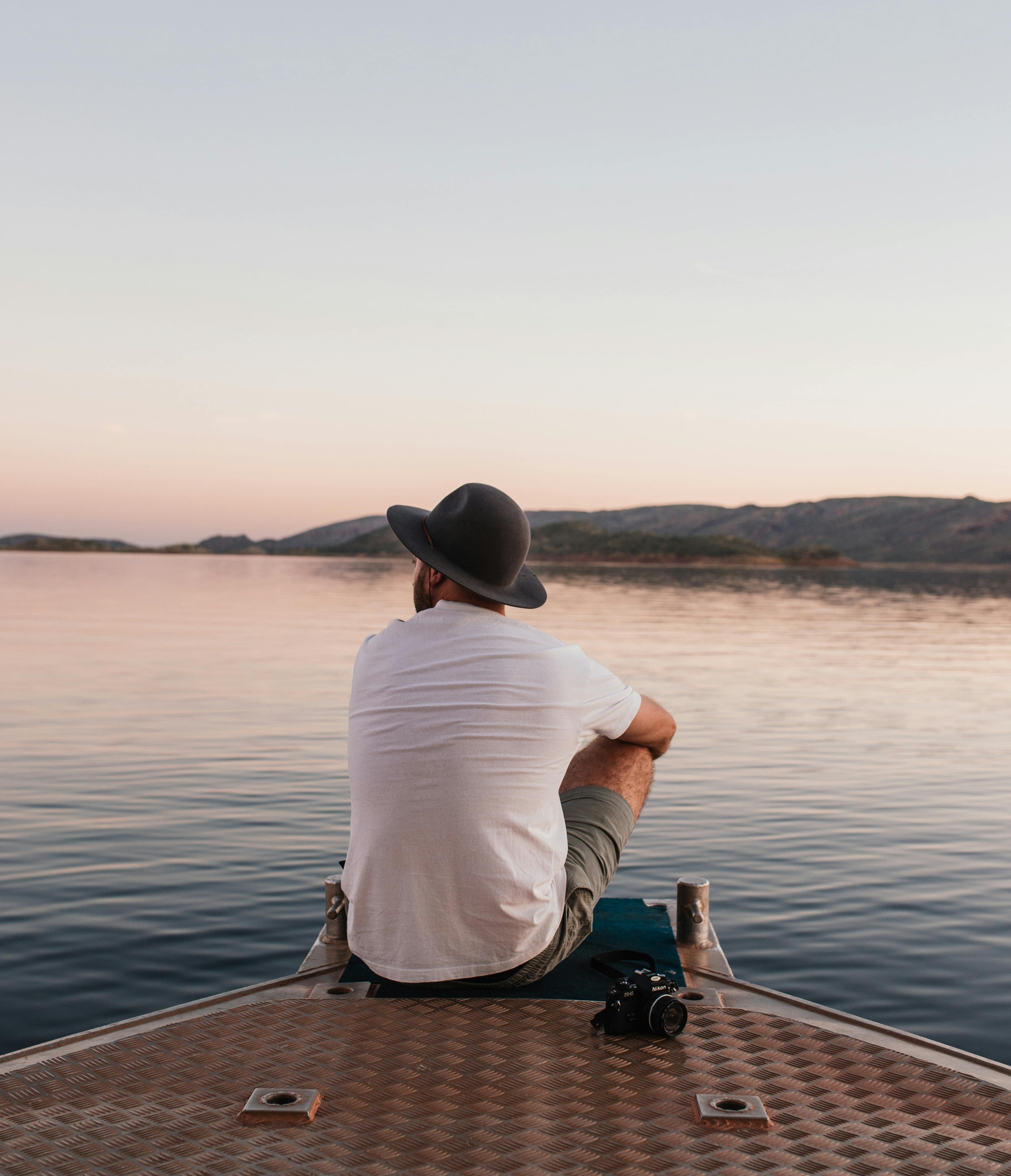 Man sitting on dock near rippling water at sunset · Free Stock Photo
