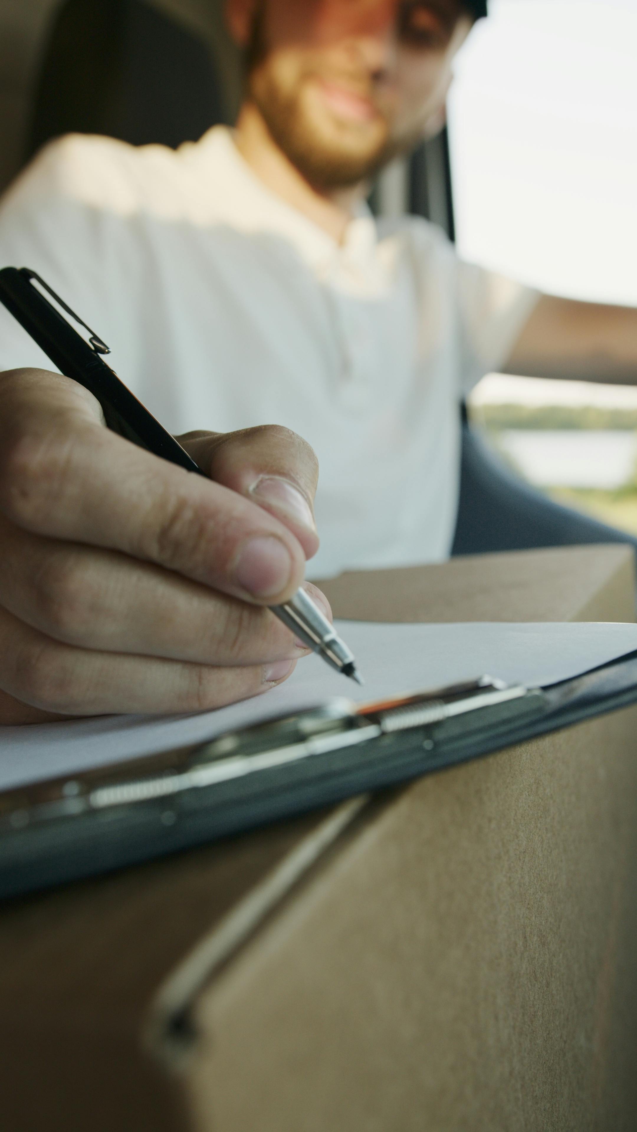 Person in Black Suit Writing on White Paper Clipped on a Clipboard ...
