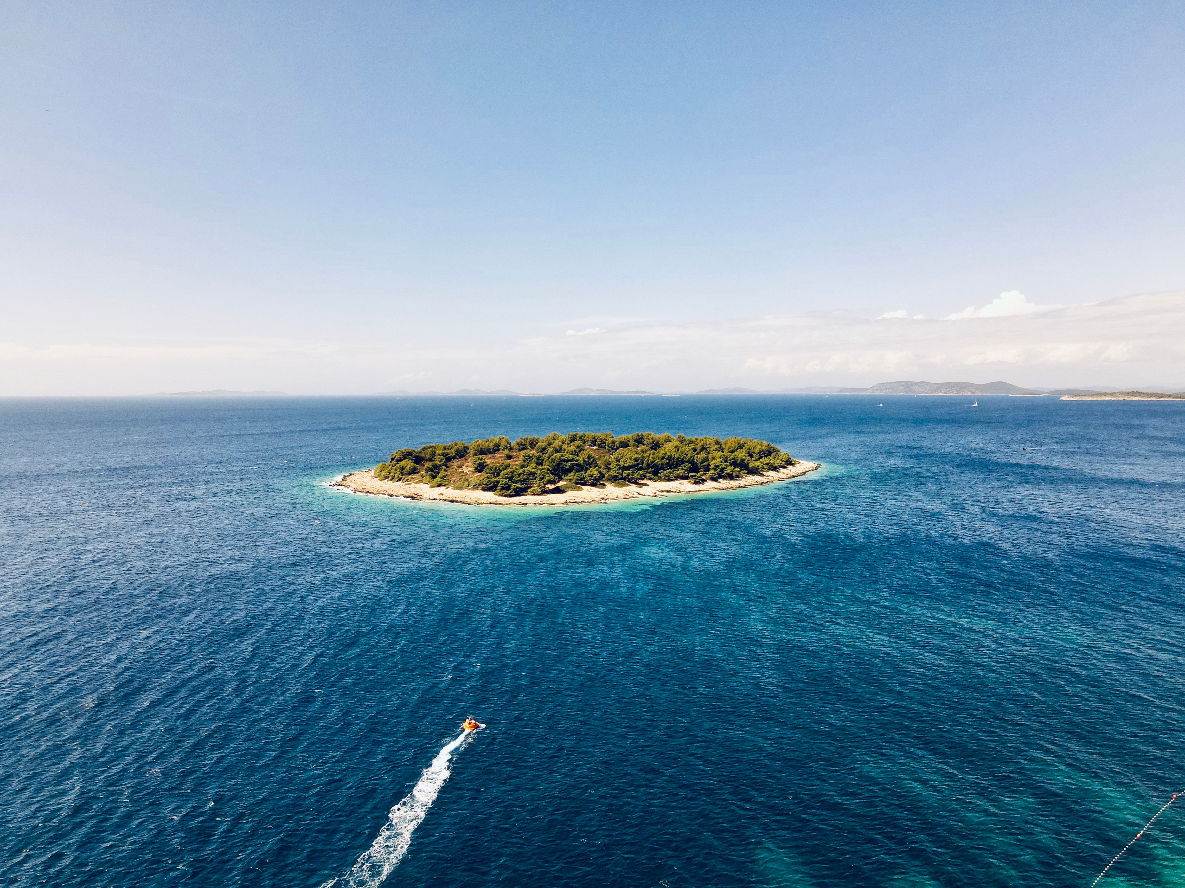 Small island in sea near sailing motorboat under sky · Free Stock Photo
