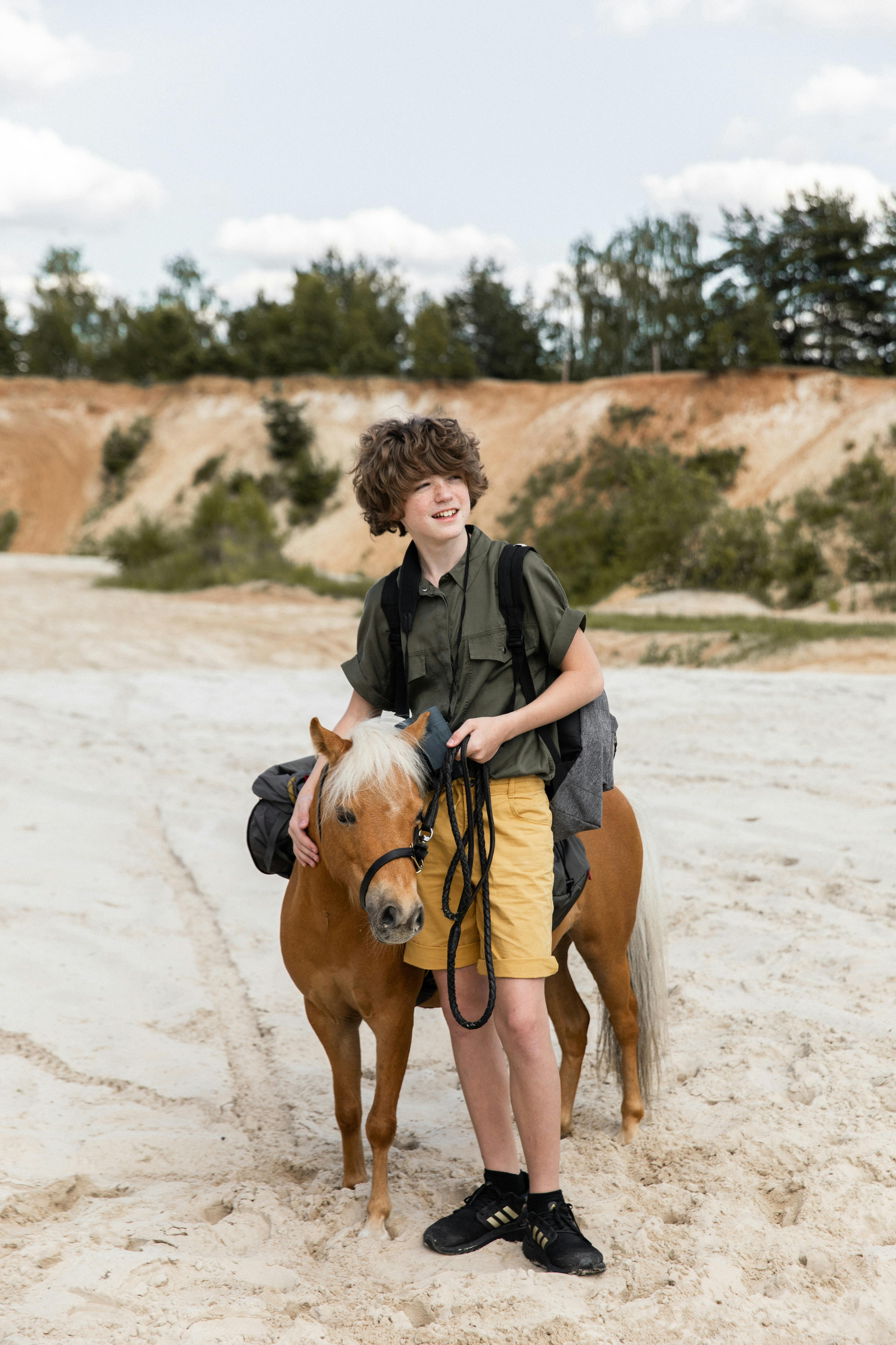Portrait of a Boy with a Mule Standing on Sand · Free Stock Photo