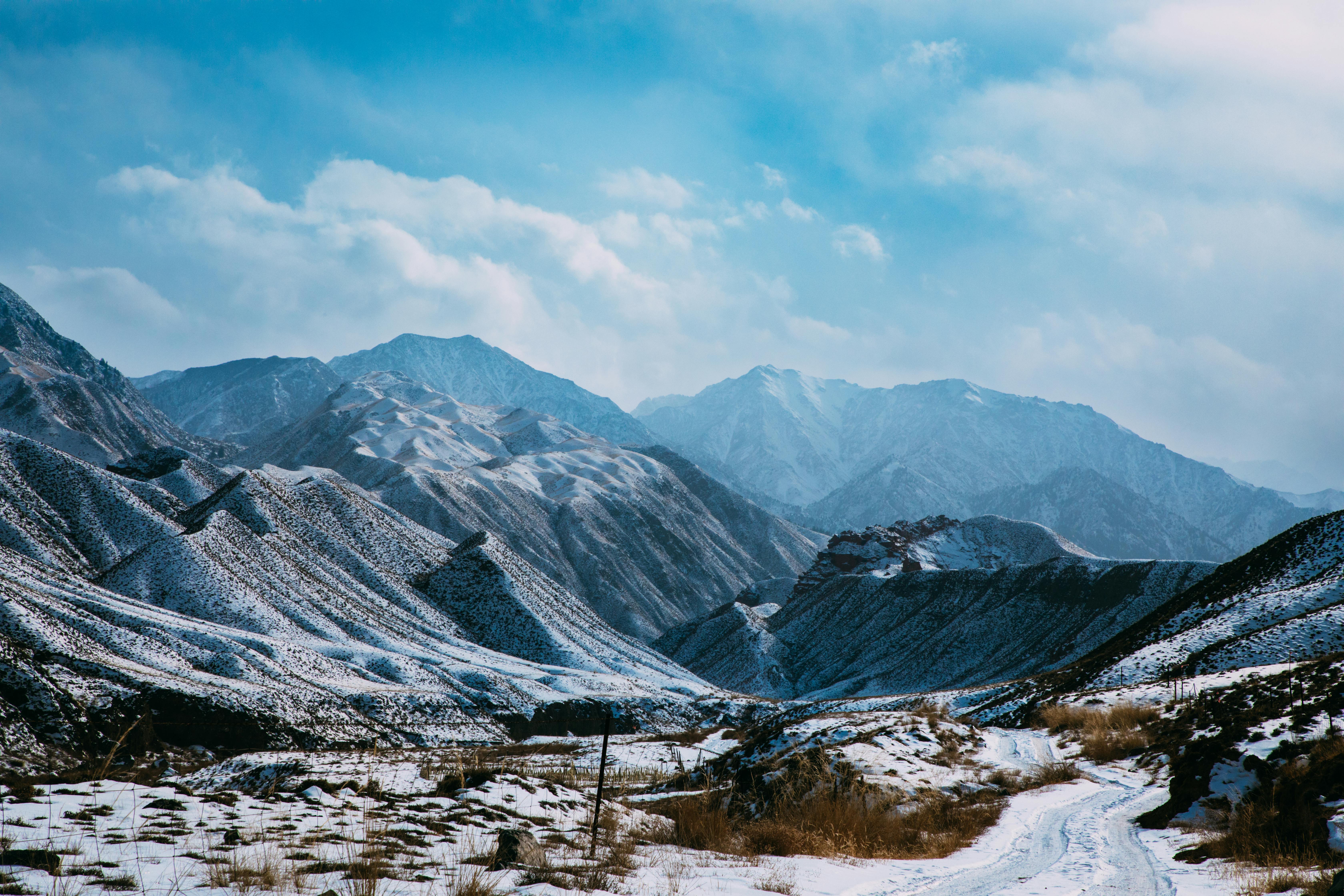 Rough snowy mountains near wavy pathway under sky · Free Stock Photo
