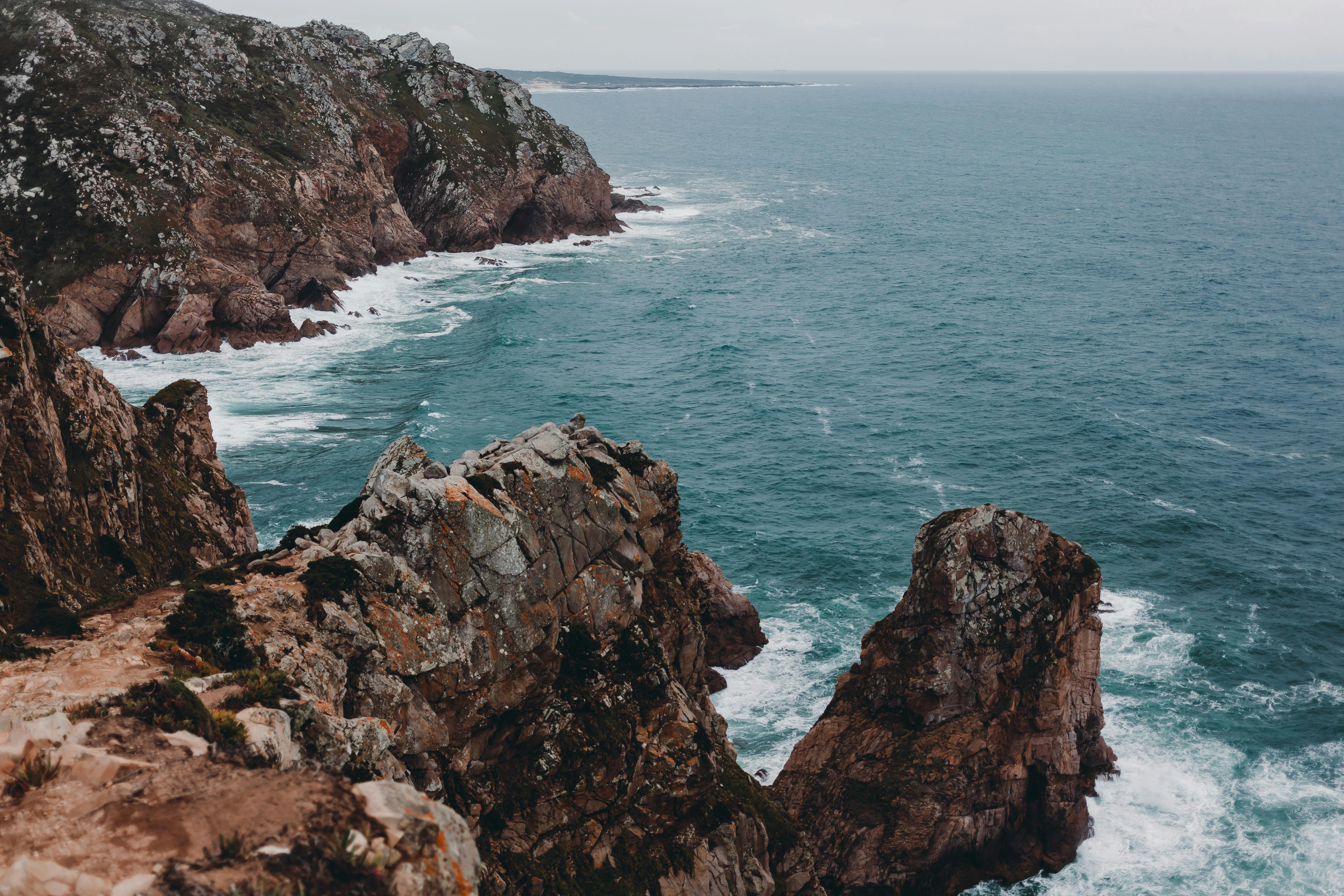 Rocky cliff above sea water in daylight · Free Stock Photo