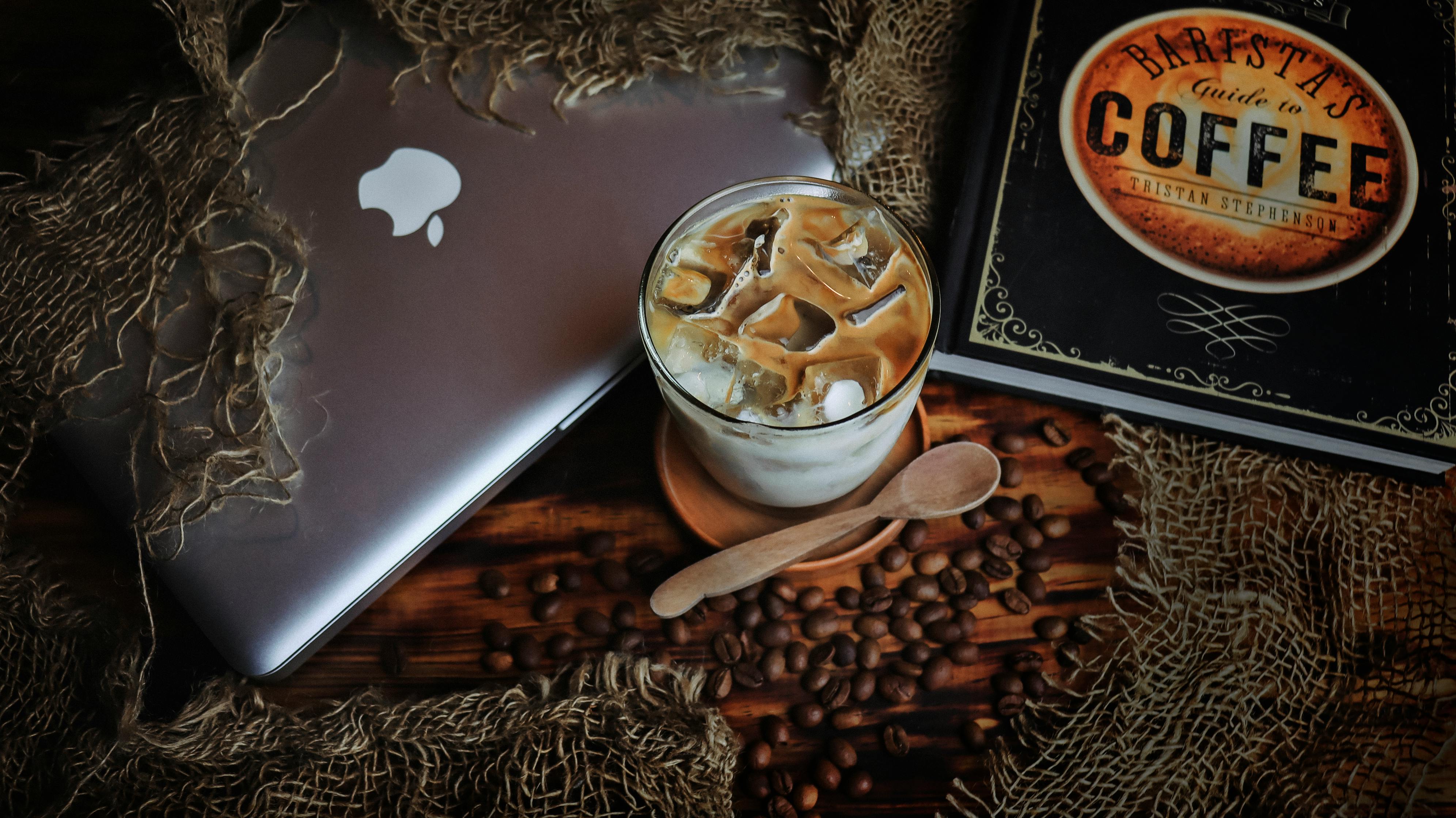 Close-Up Shot of a Glass of Iced Coffee beside a Macbook · Free Stock Photo