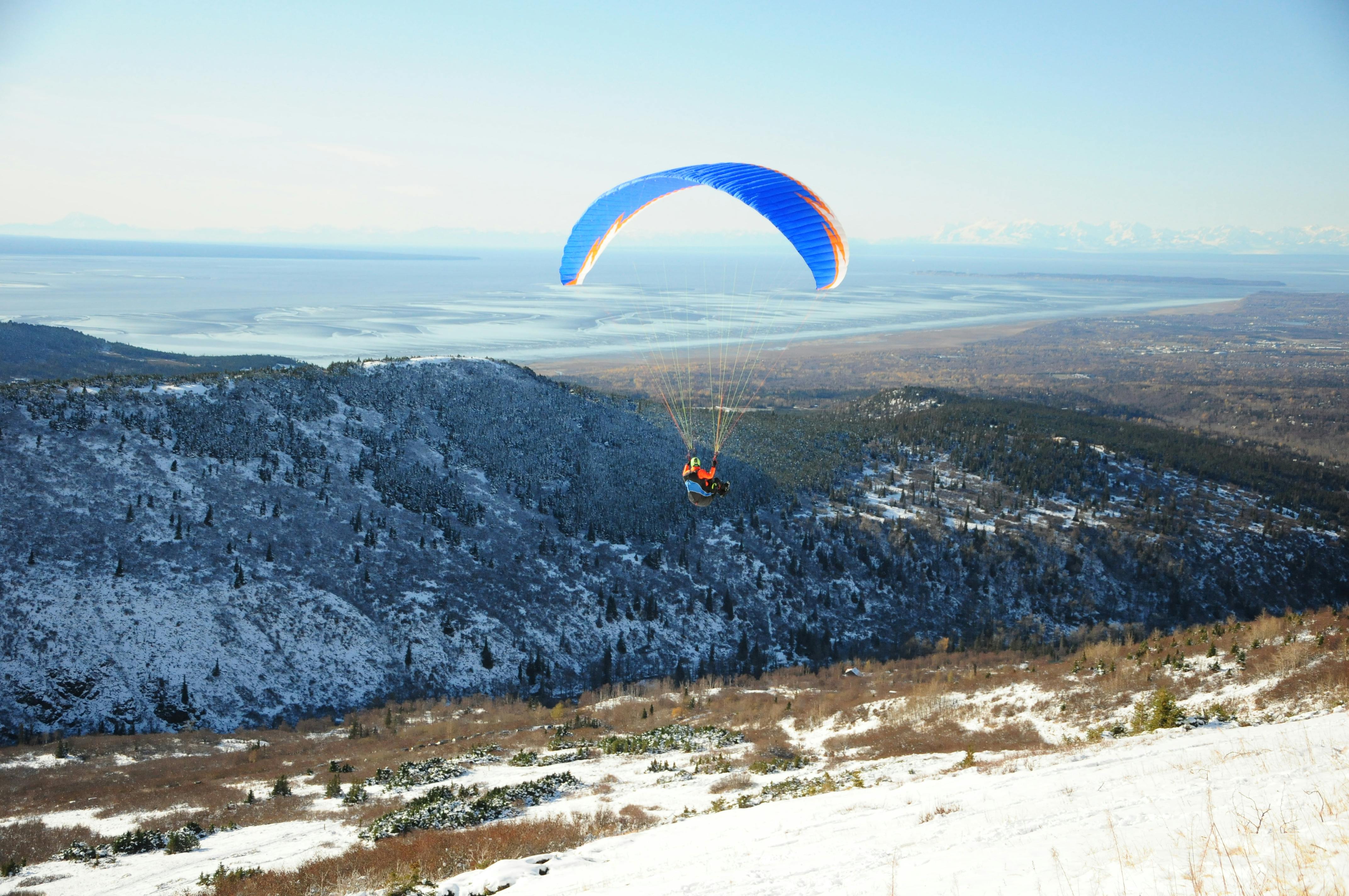 Person on a Paraglider Over Snowy Hills · Free Stock Photo