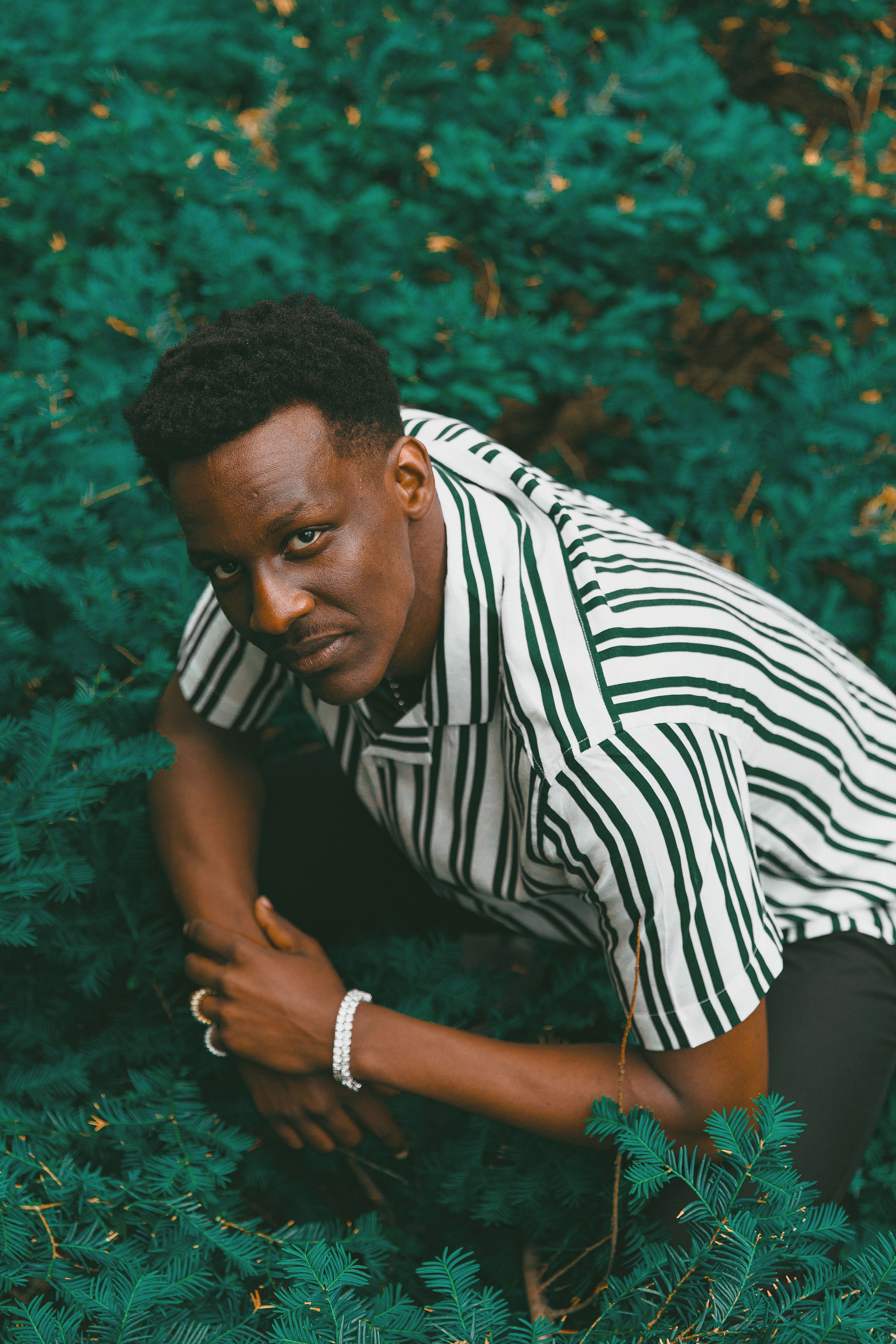 Emotionless black man hunkering on green lawn · Free Stock Photo