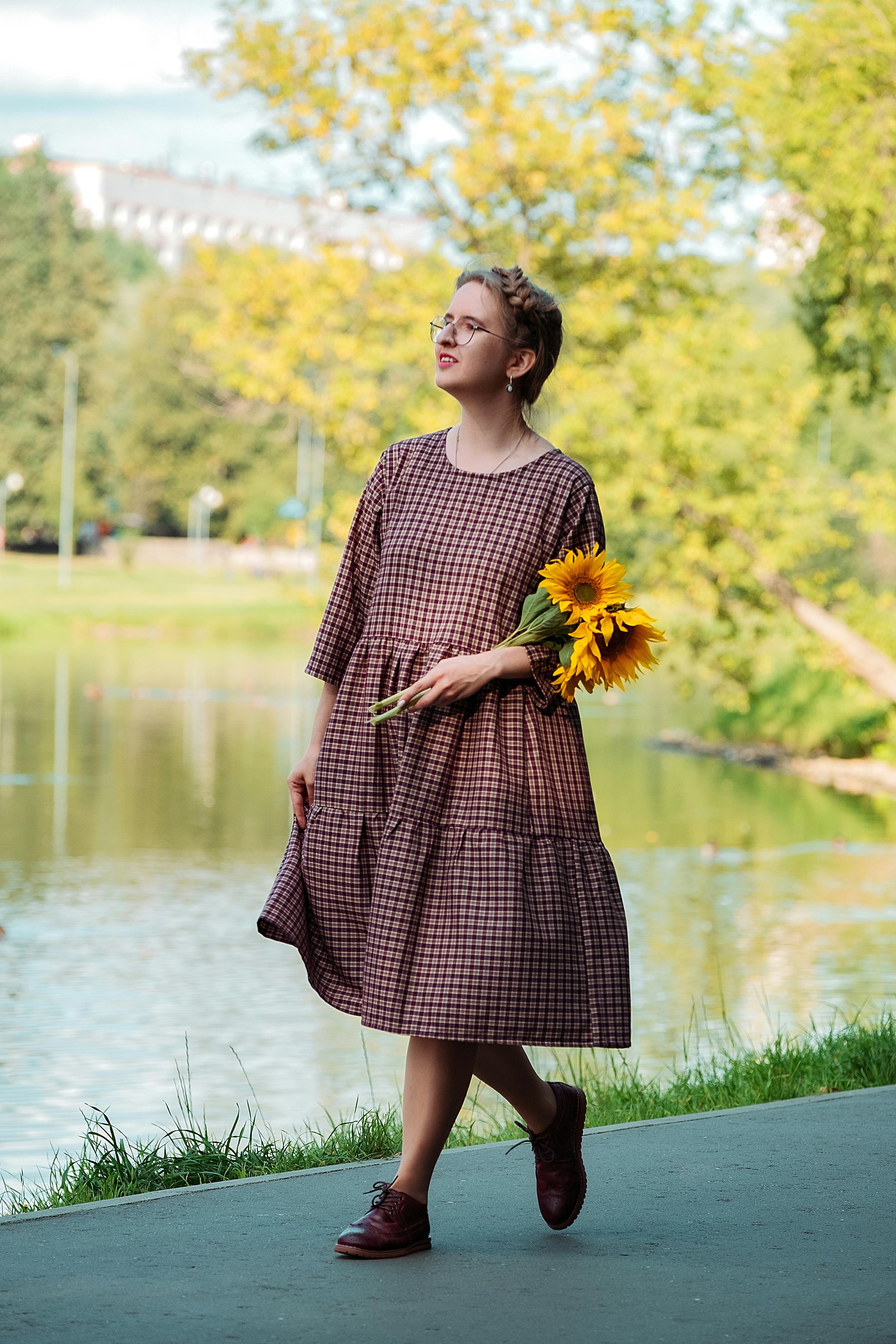 Cheerful woman with bunch of sunflowers walking on tranquil lakeside ...