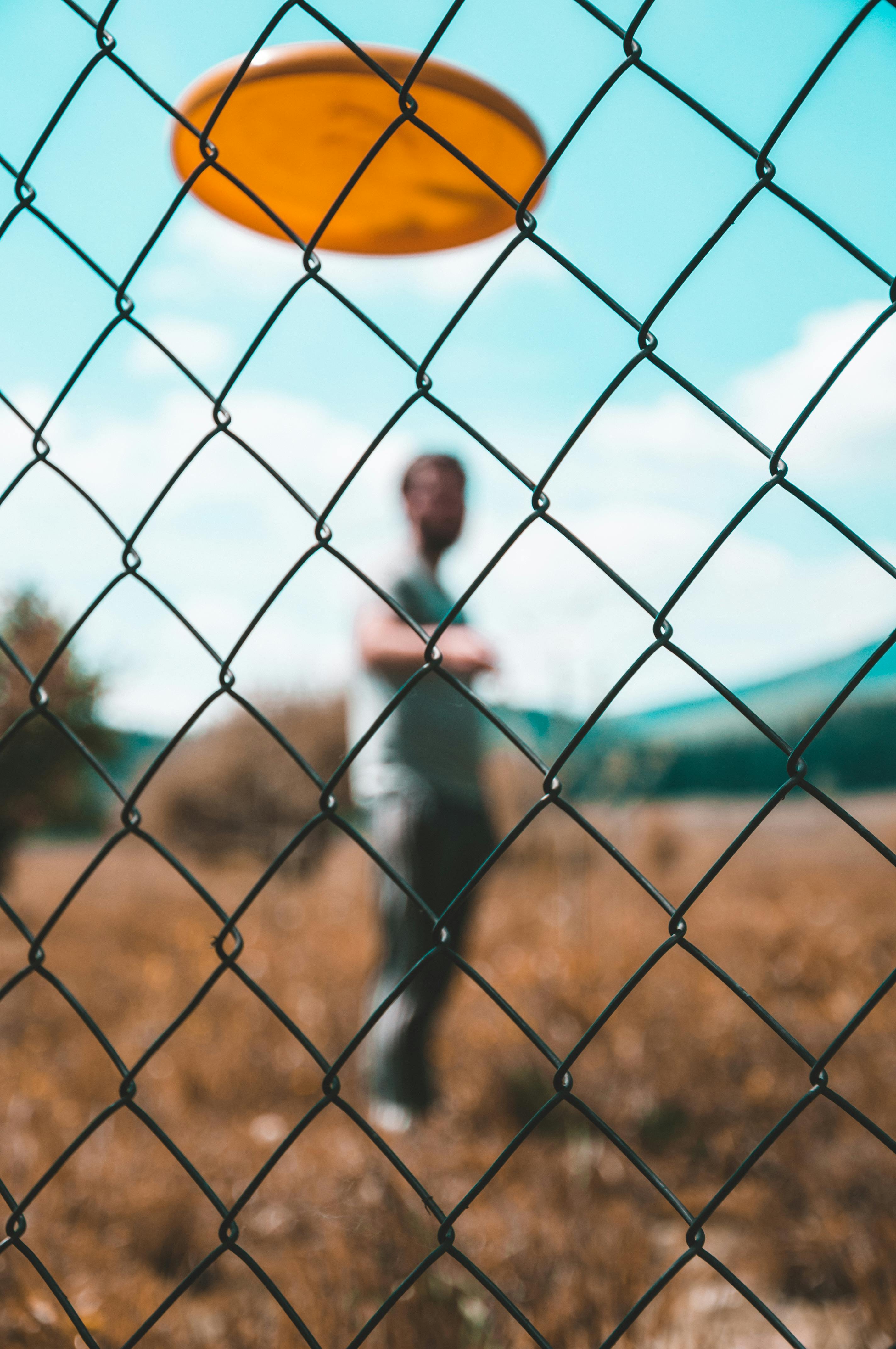 Photo of a Man Throwing a Disk behind a Netted Fence · Free Stock Photo
