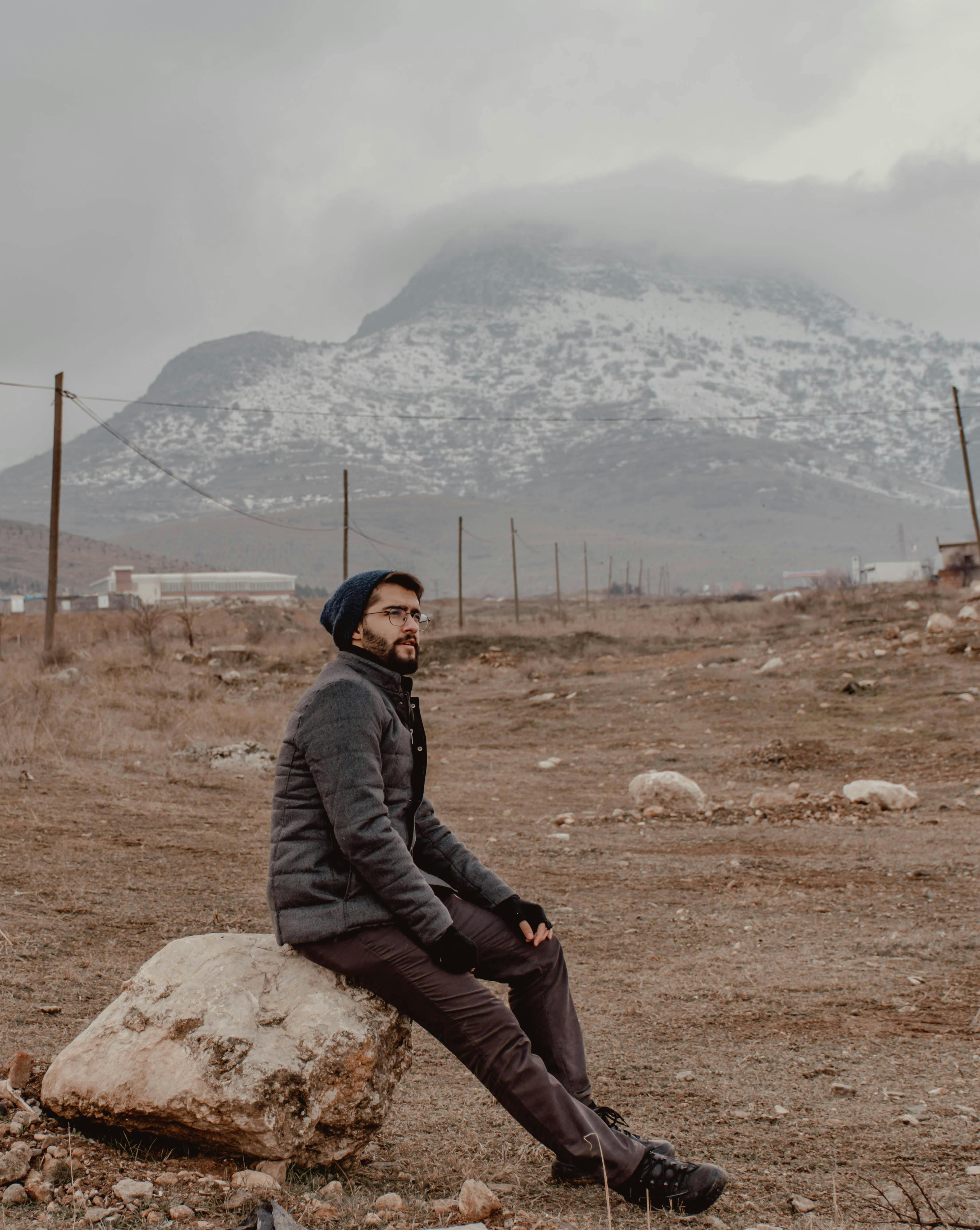 Man in Brown Jacket Standing on Big Rocks Near the Shore · Free Stock Photo