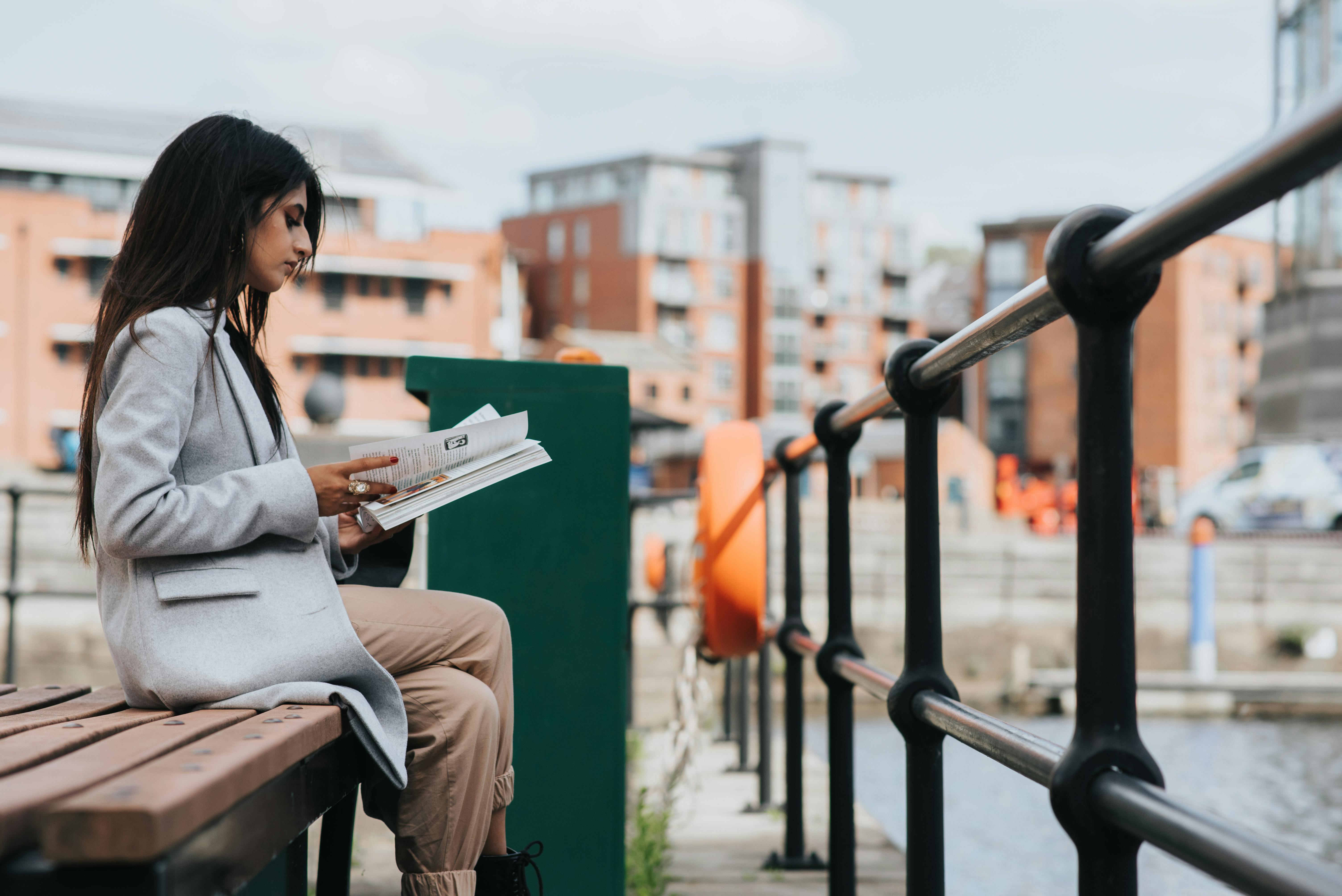 Serious ethnic stylish lady reading magazine on bench · Free Stock Photo