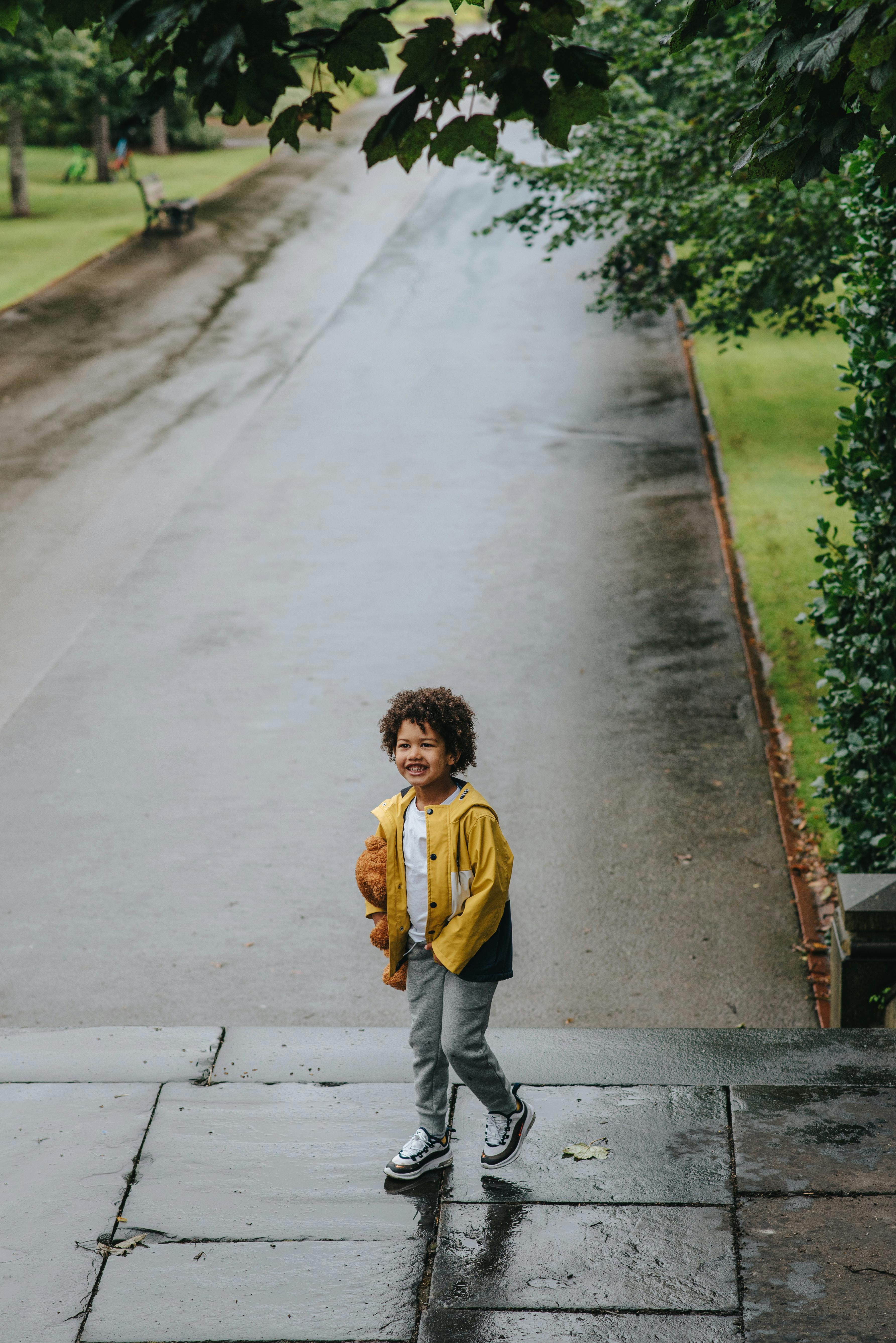 Cheerful ethnic boy walking on wet pavement in city park · Free Stock Photo