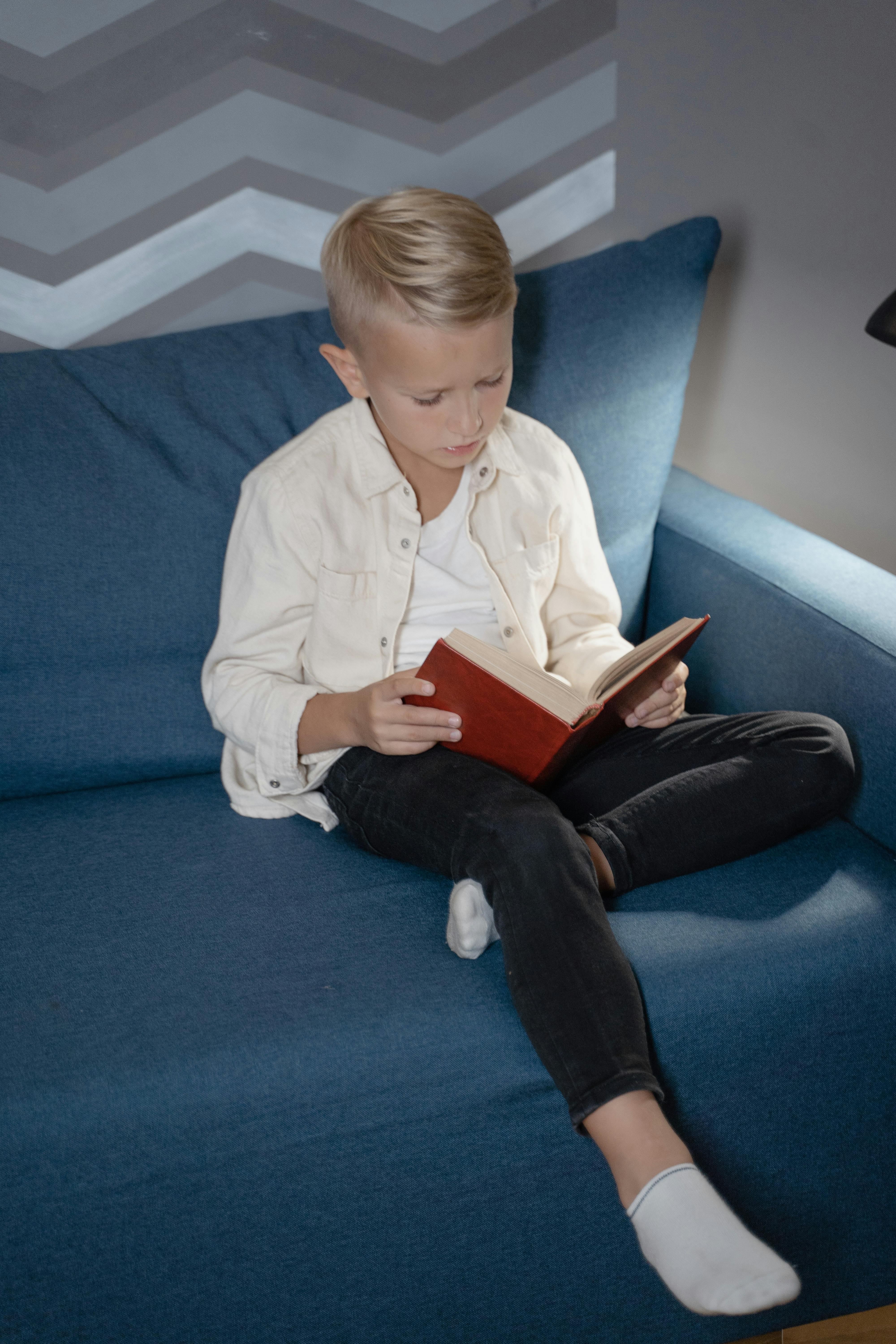 Kid Sitting on a Sofa Reading a Book · Free Stock Photo