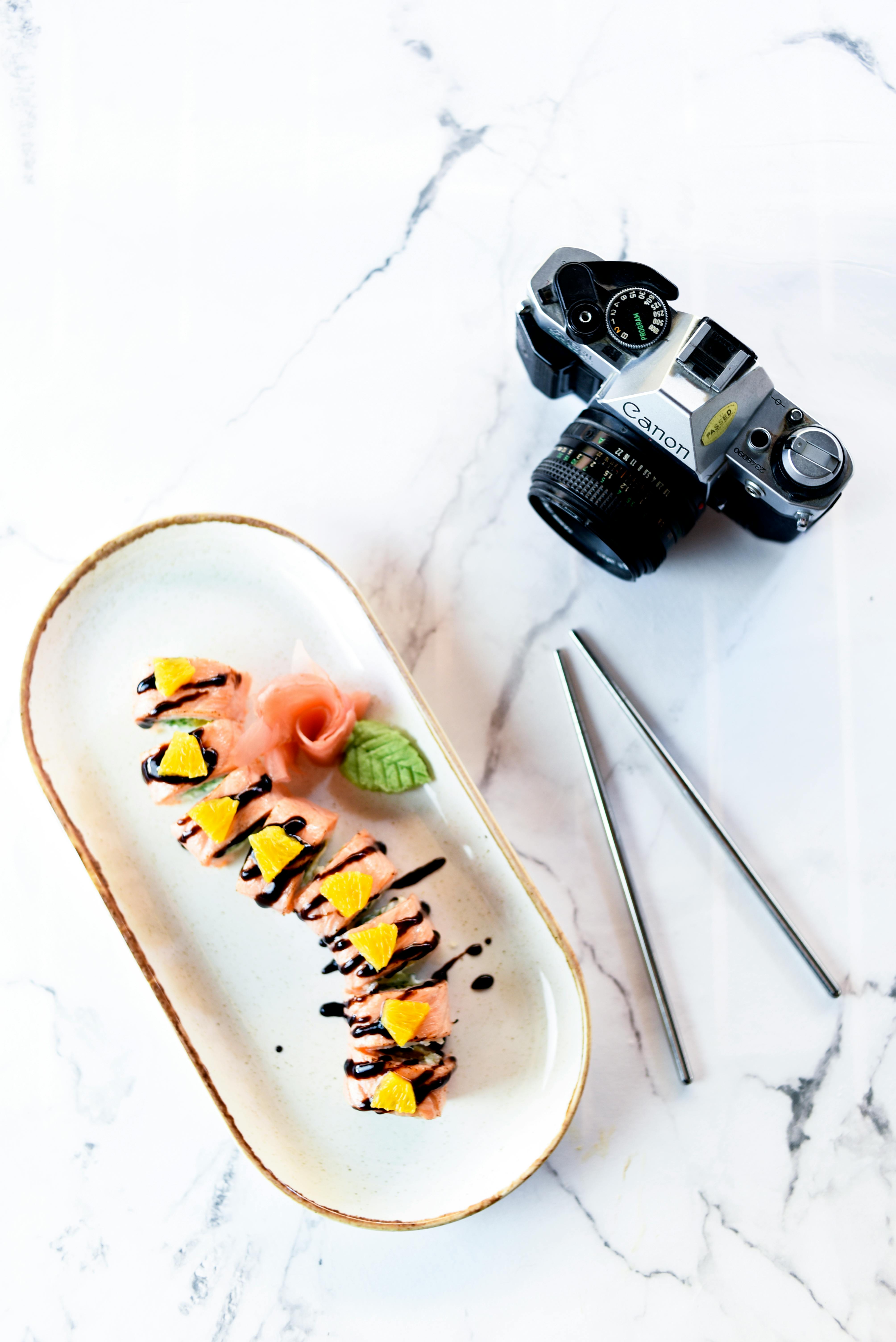 Black Canon Camera Beside a Plate of Sushi on a Marbled Surface · Free ...