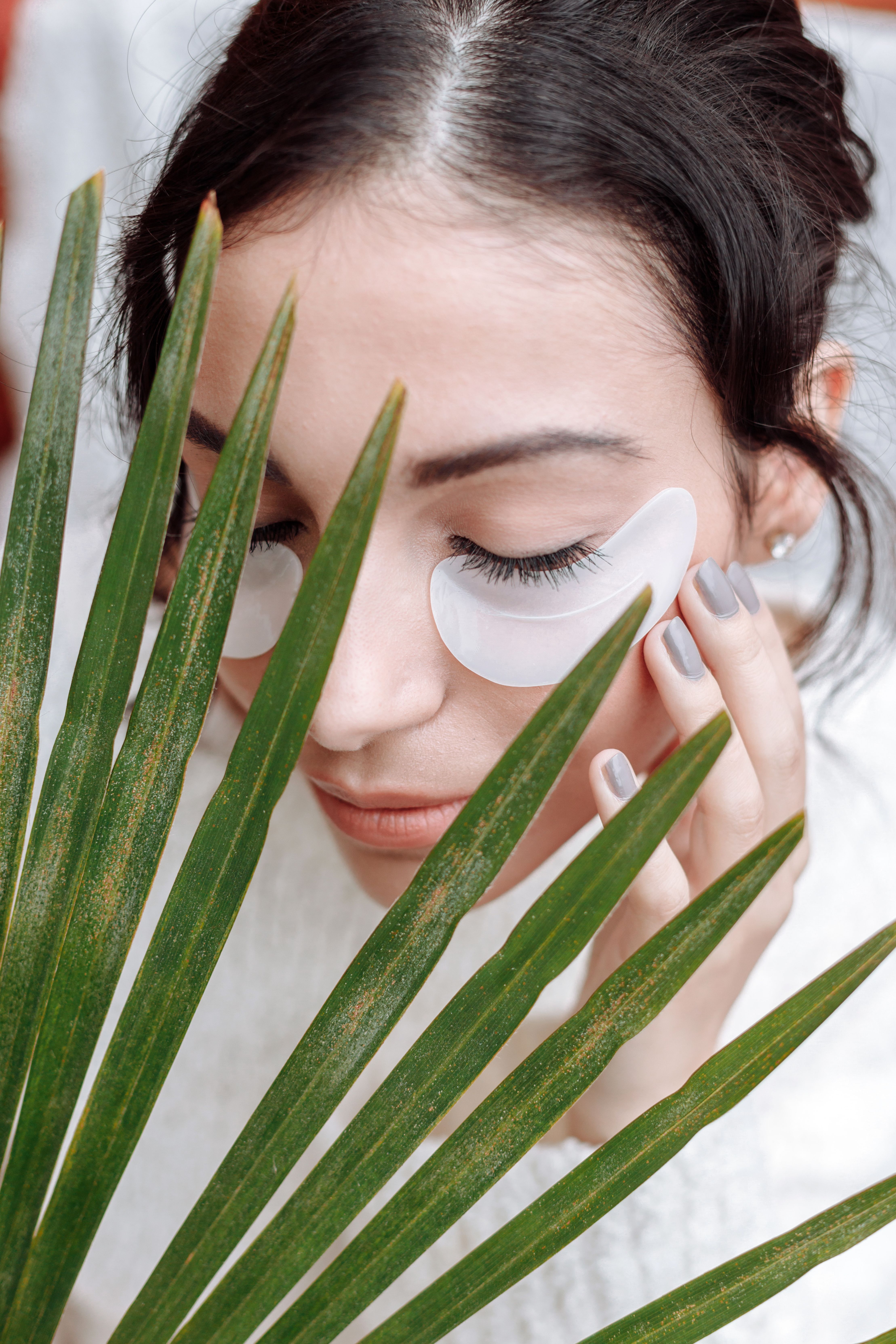 Woman Behind Green Leaves Wearing Under Eye Masks · Free Stock Photo