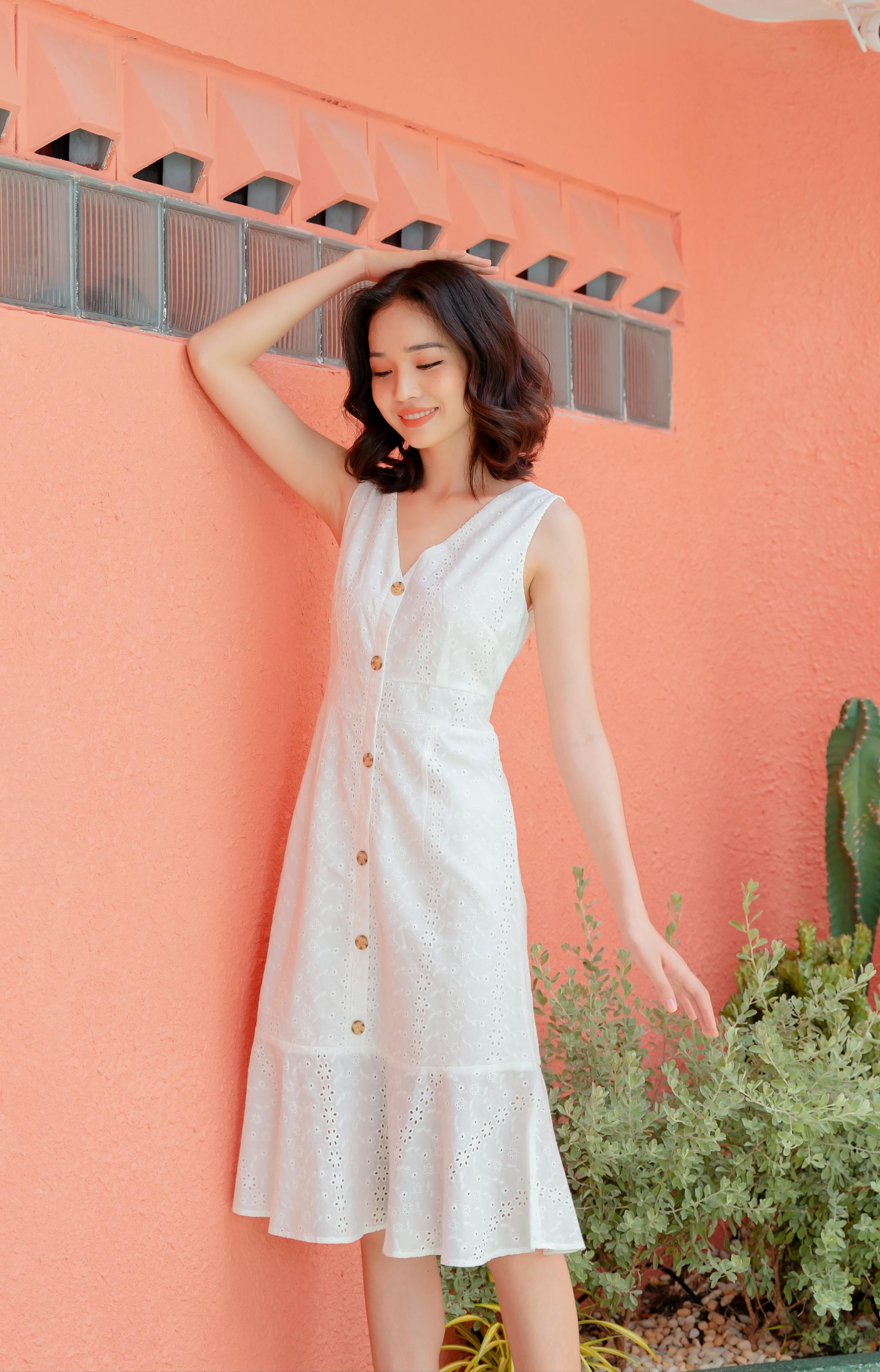 Stylish young Asian woman touching head while standing near pink wall ...