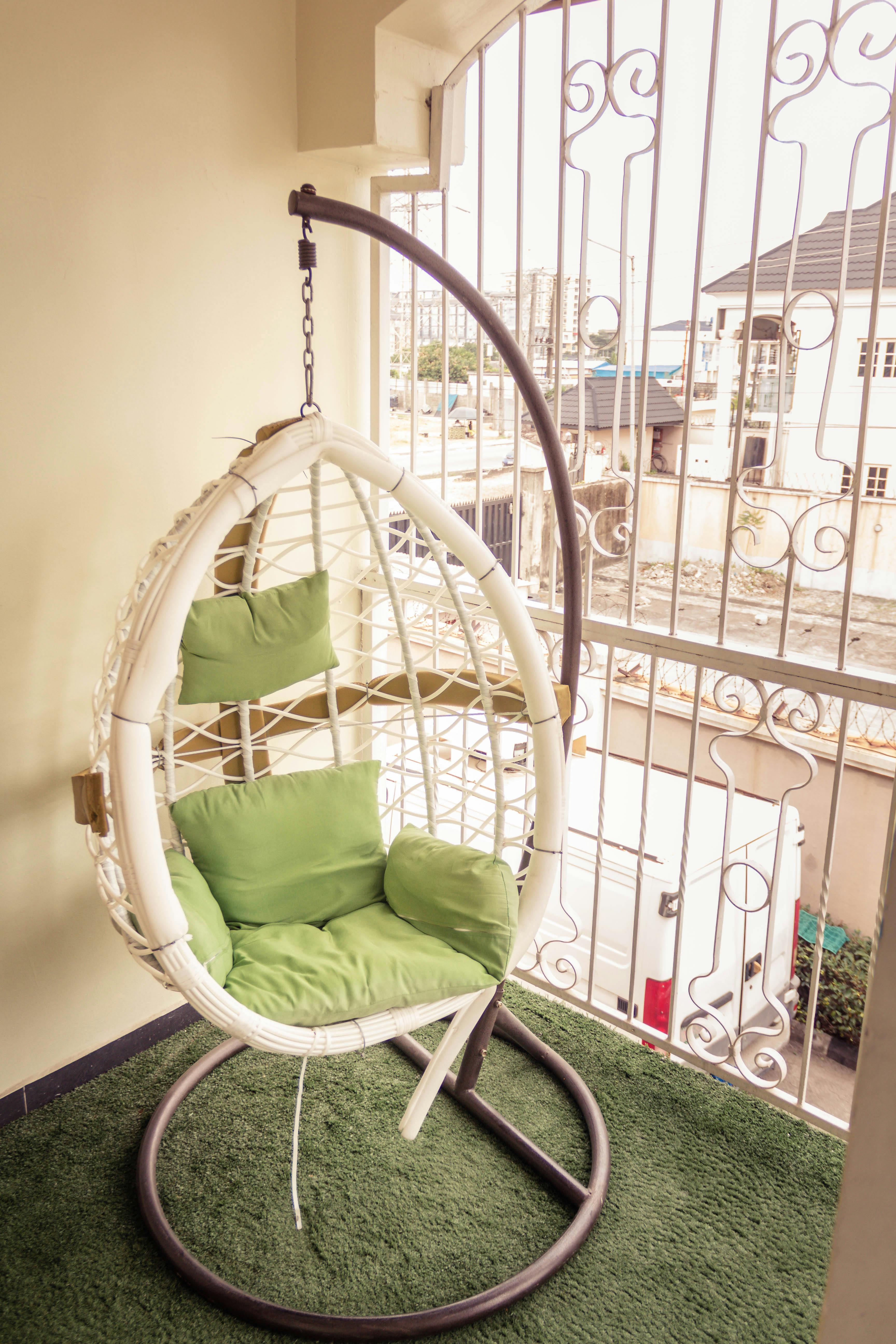 A White Cocoon Chair wit Green Cushions in the Balcony · Free Stock Photo