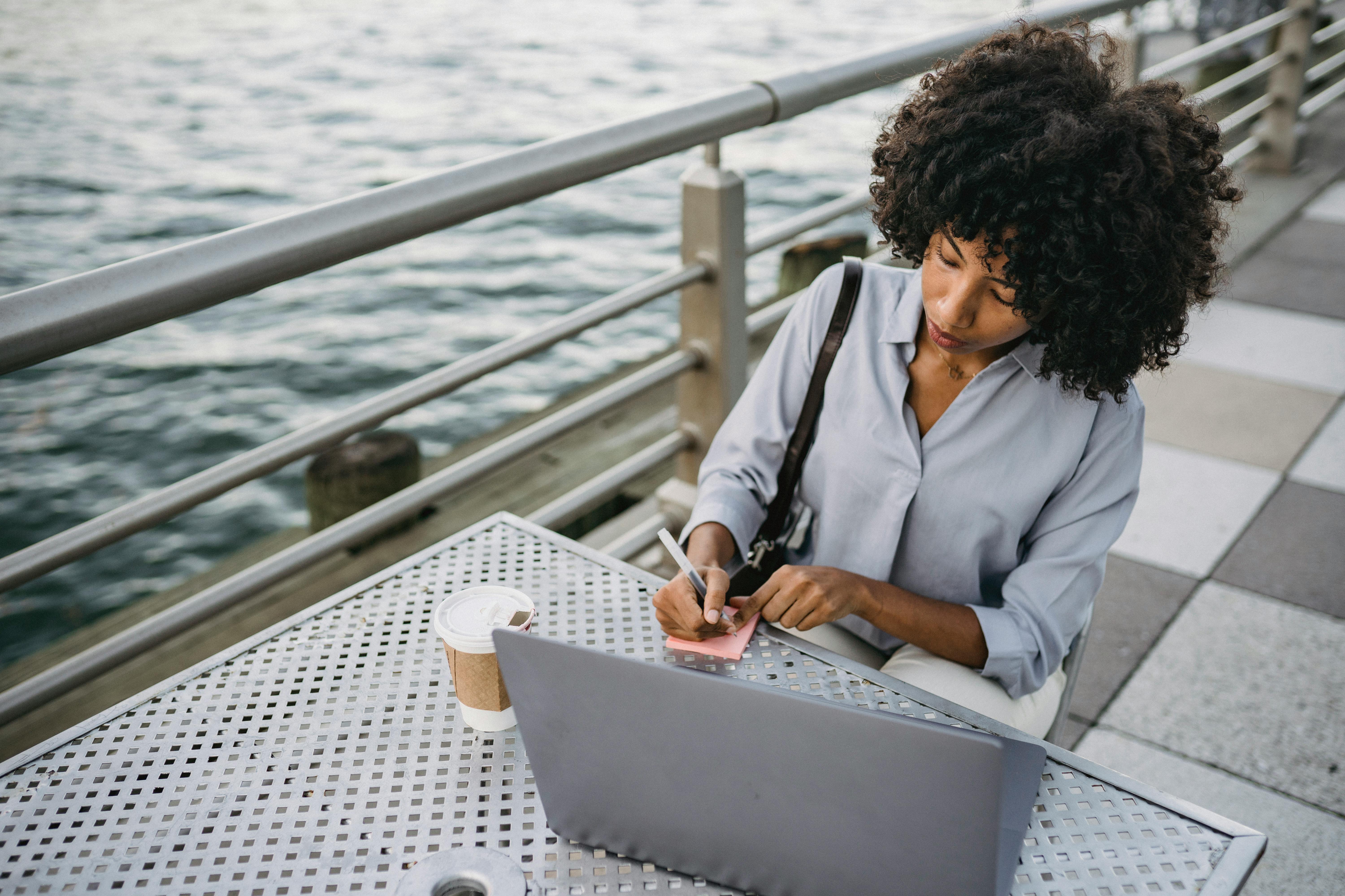 Photograph of a Woman with Curly Hair Writing on a Pink Sticky Note ...