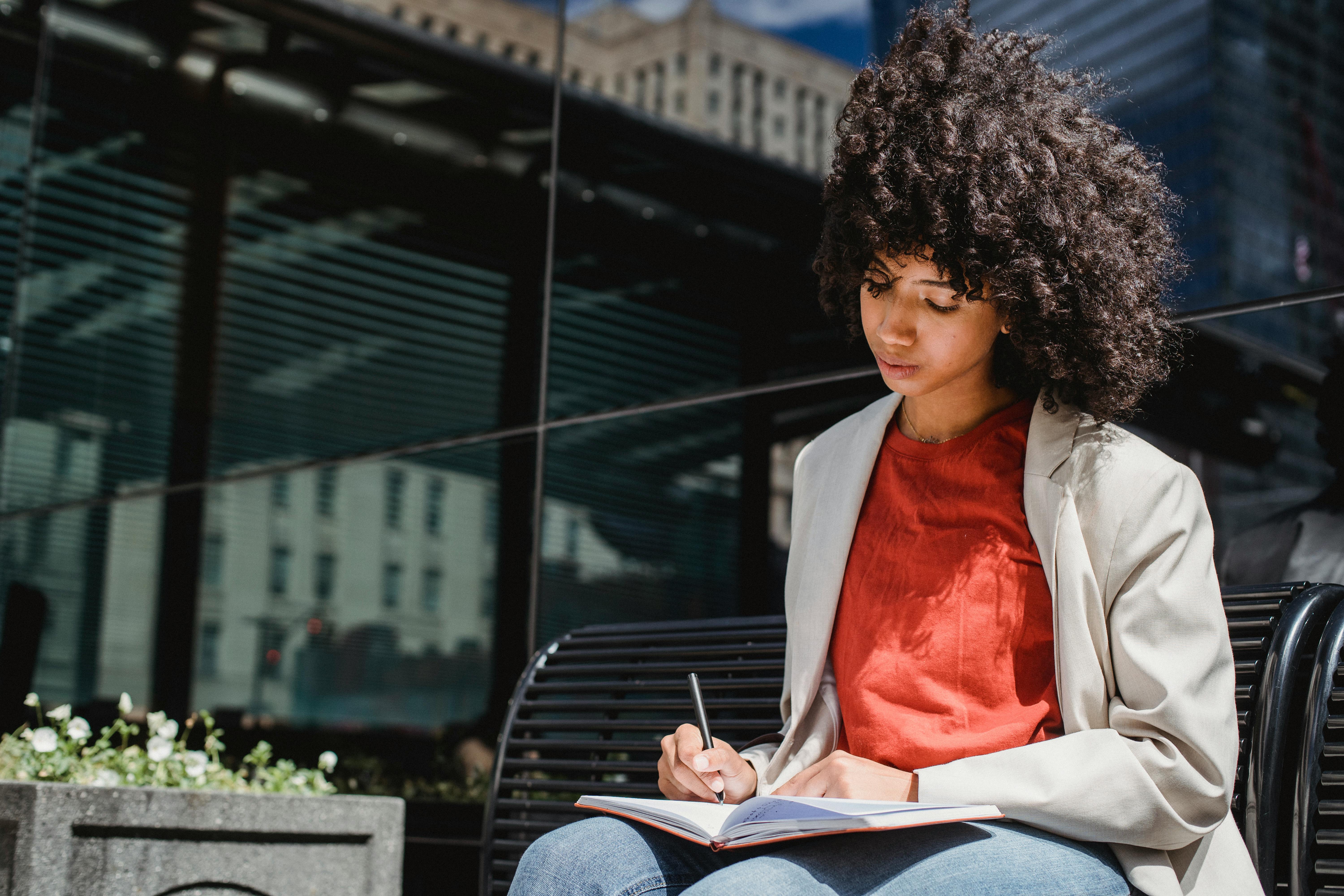 A Woman Sitting on the Bench Writing on a Notebook · Free Stock Photo