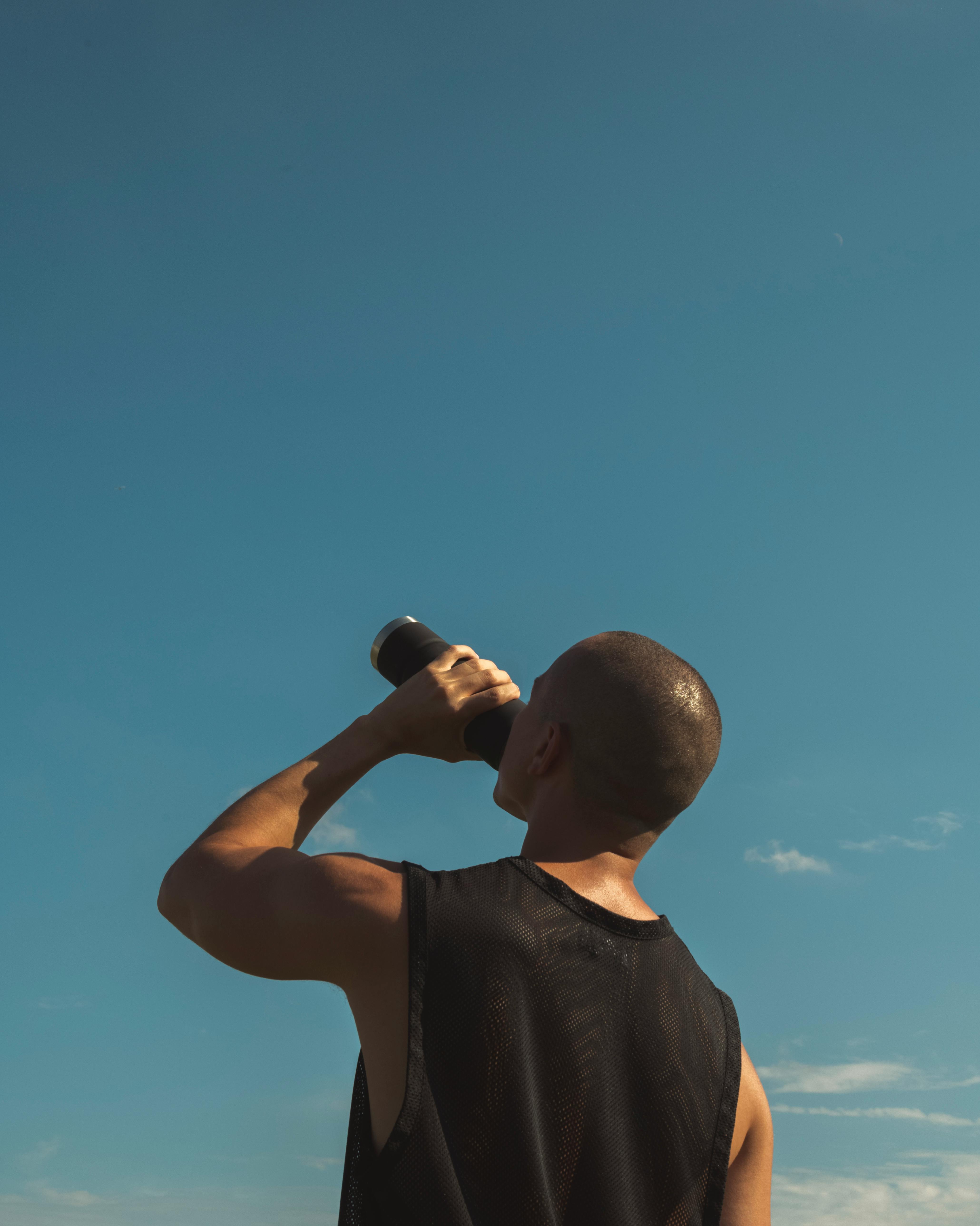 Man Drinking from Black Water Tumbler Under Blue Sky · Free Stock Photo