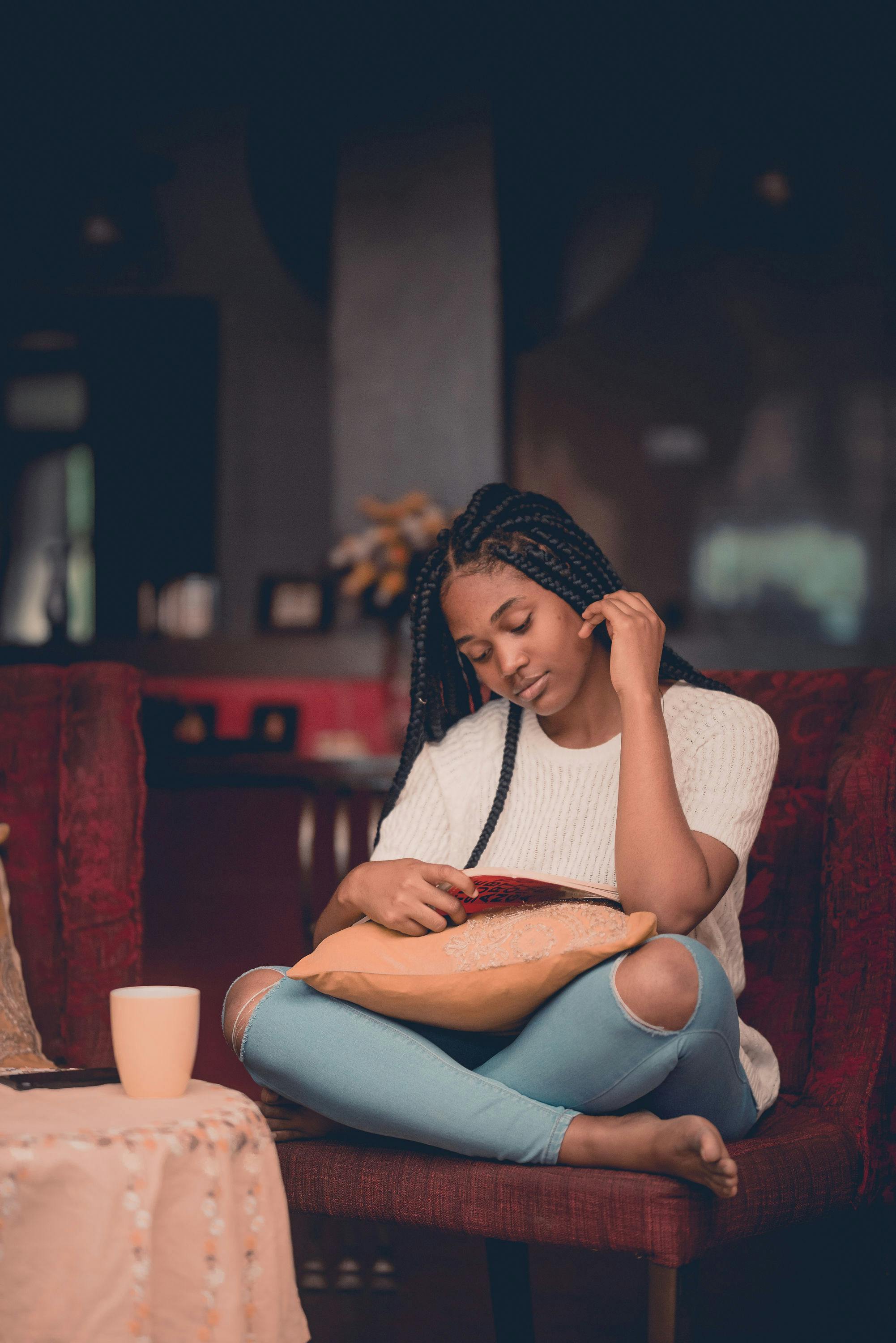 A Woman Sitting on a Chair While Reading a Book · Free Stock Photo