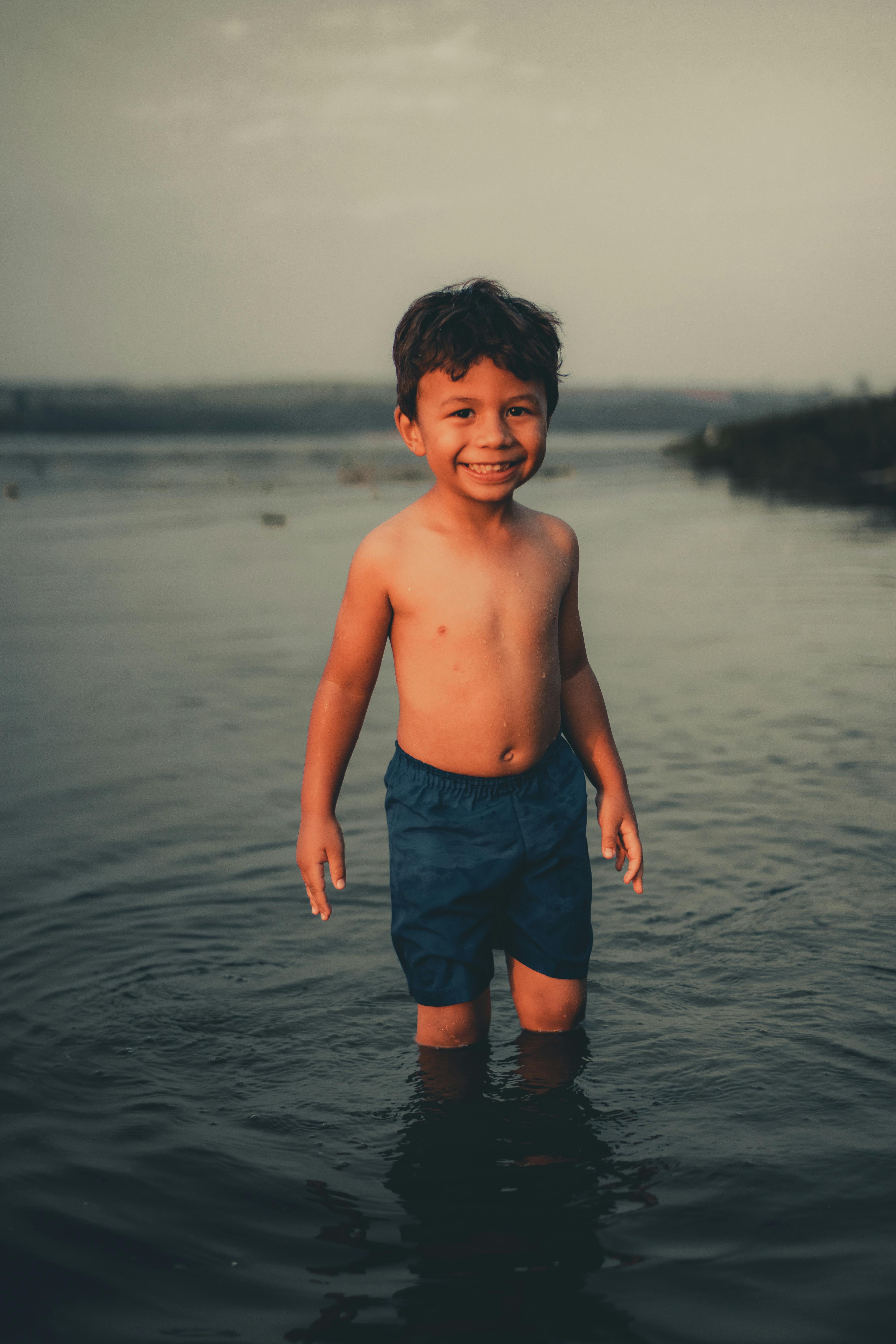 A Shirtless Boy Wearing Blue Shorts Standing on Water · Free Stock Photo