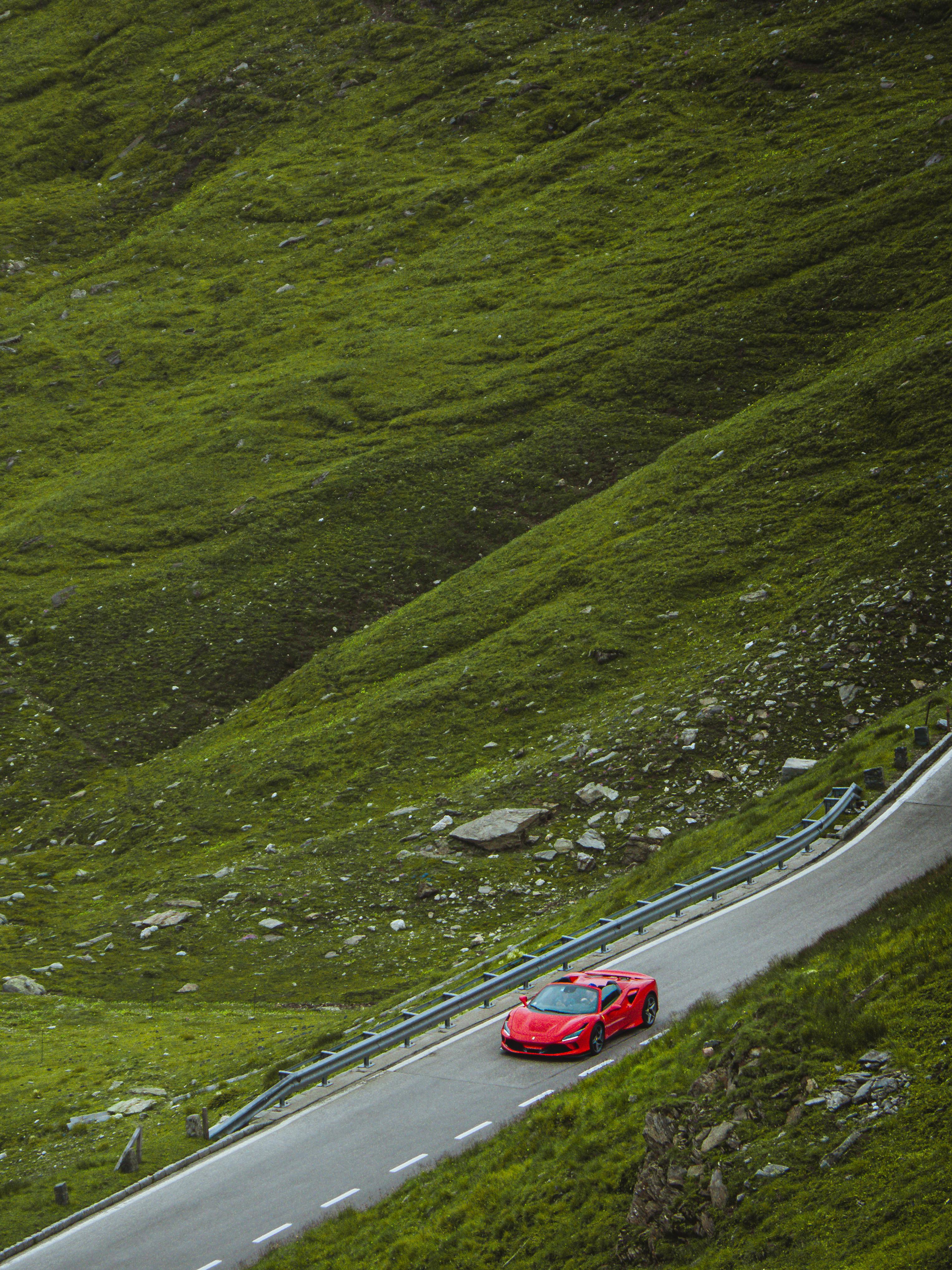 Red sports car driving on road in green valley · Free Stock Photo