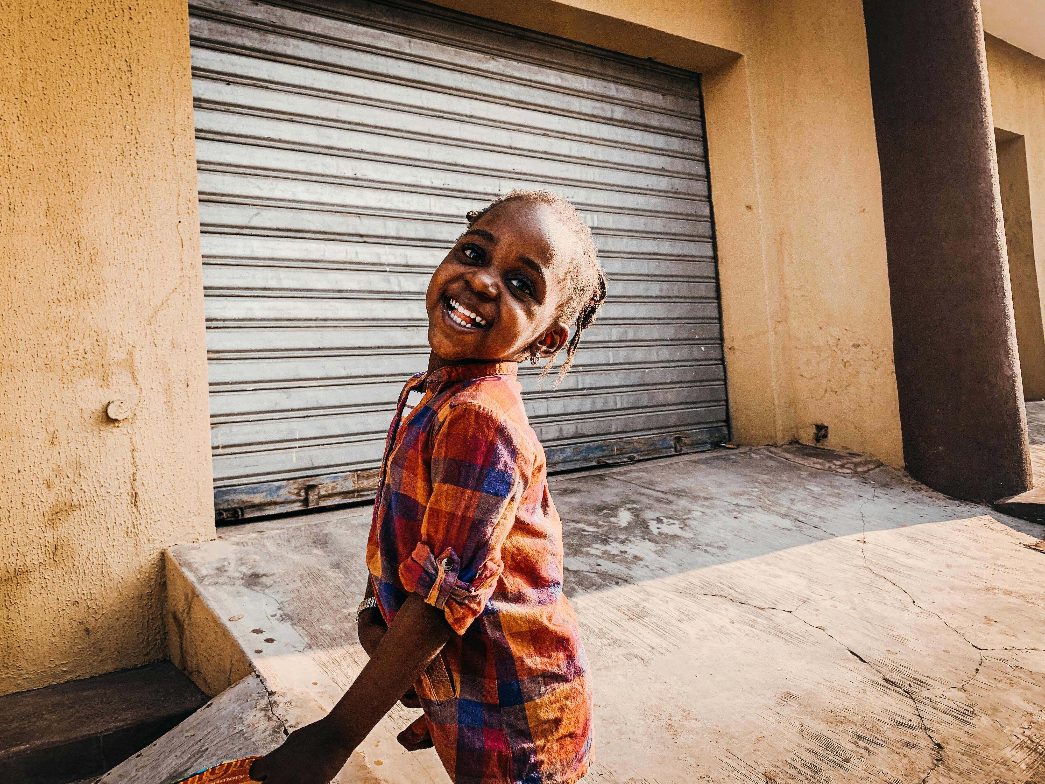 A Smiling Kid on the Street Near the Roller Shutter · Free Stock Photo