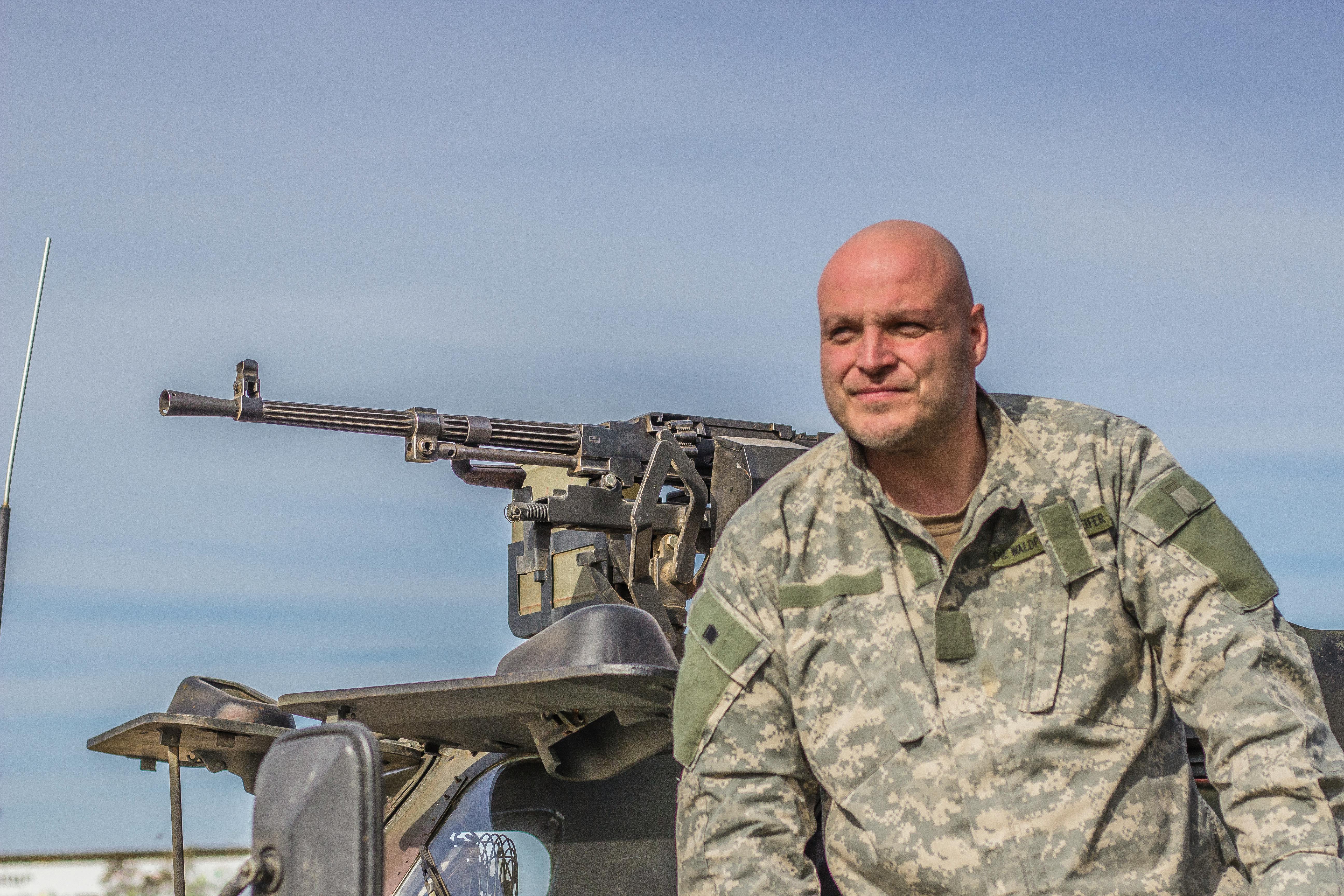 Man in US Army Uniform Siting next to Machine Gun Mounted on top of ...