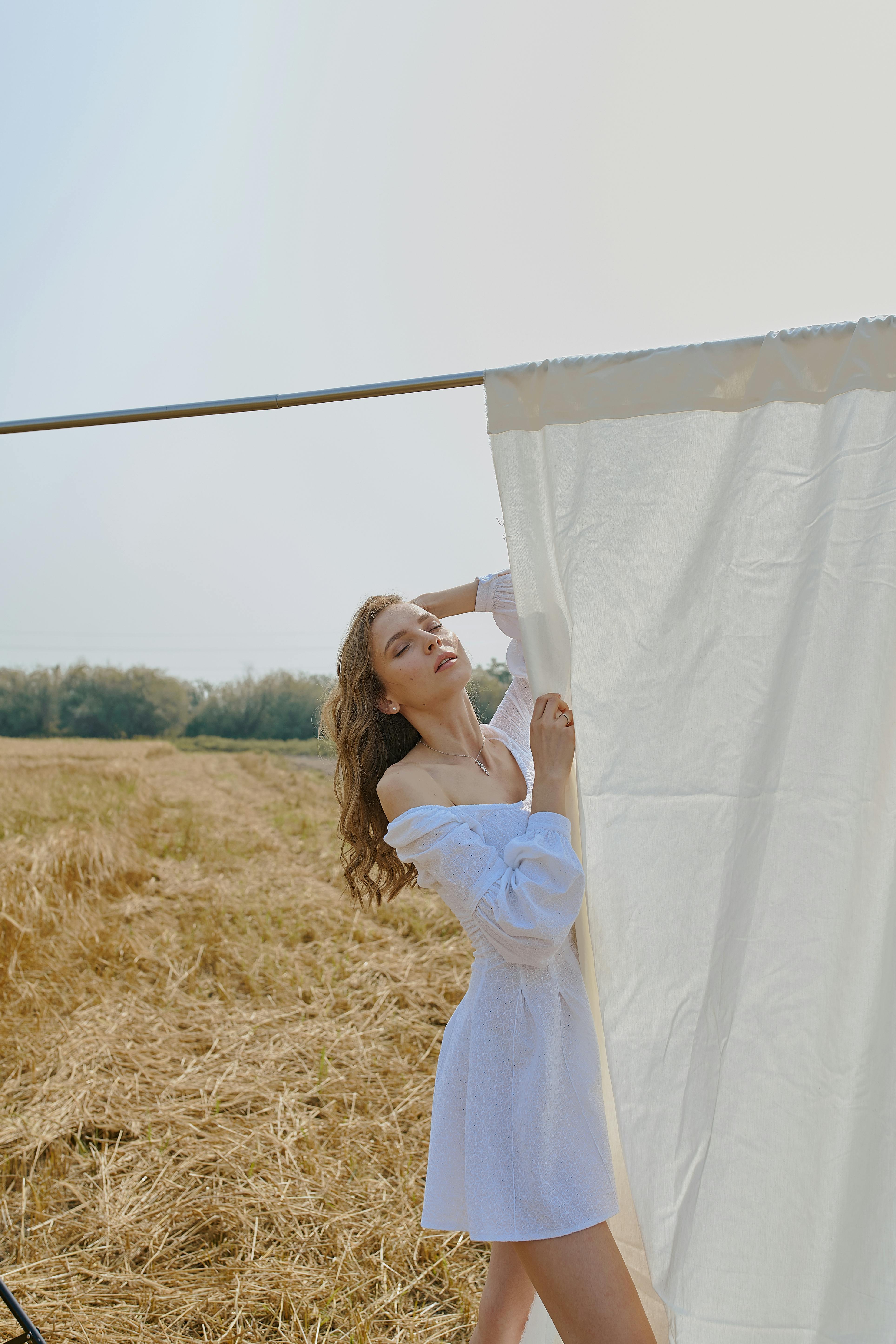 Stylish female standing near white sheet in field · Free Stock Photo