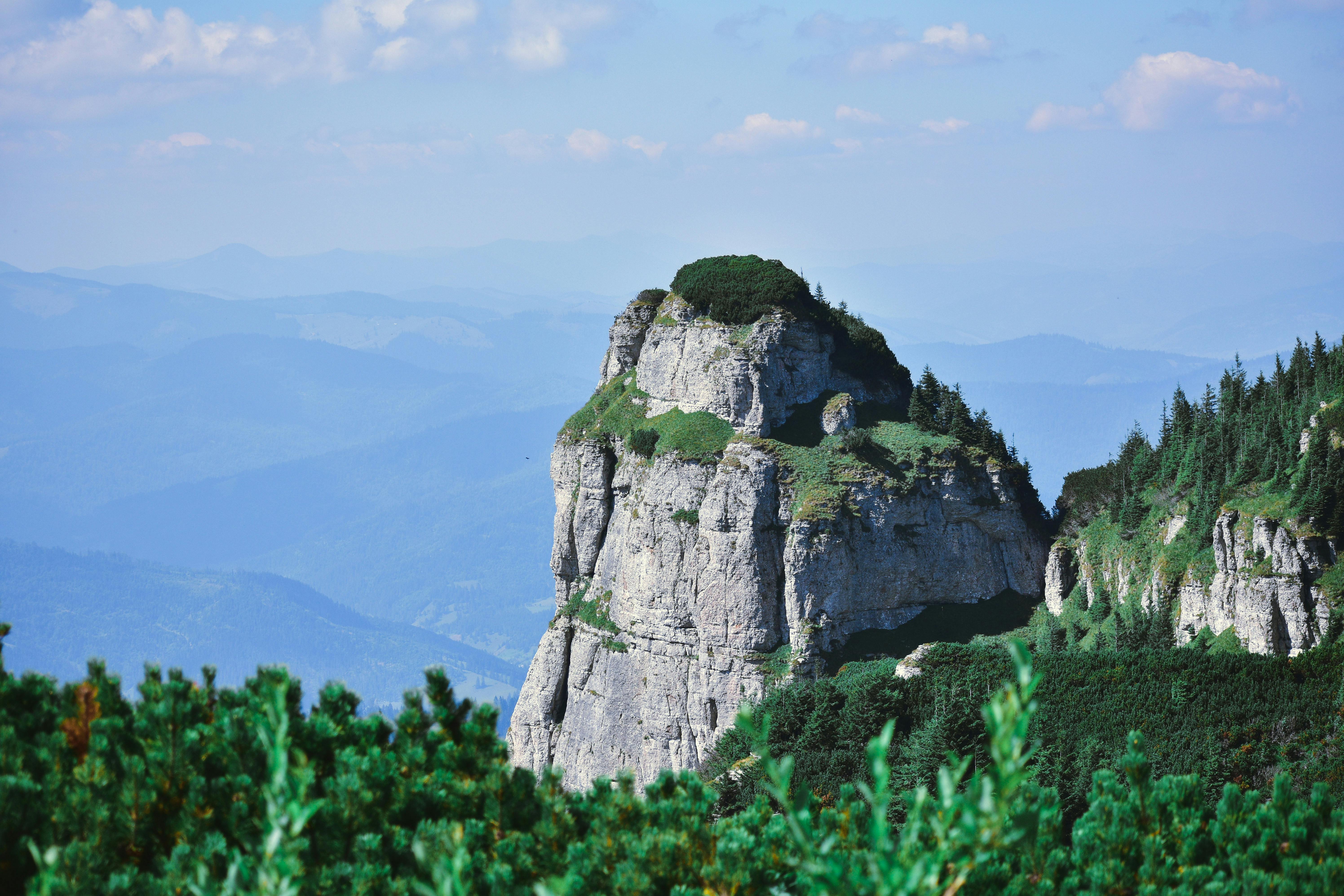 Rough rock near colorful trees under blue cloudy sky · Free Stock Photo