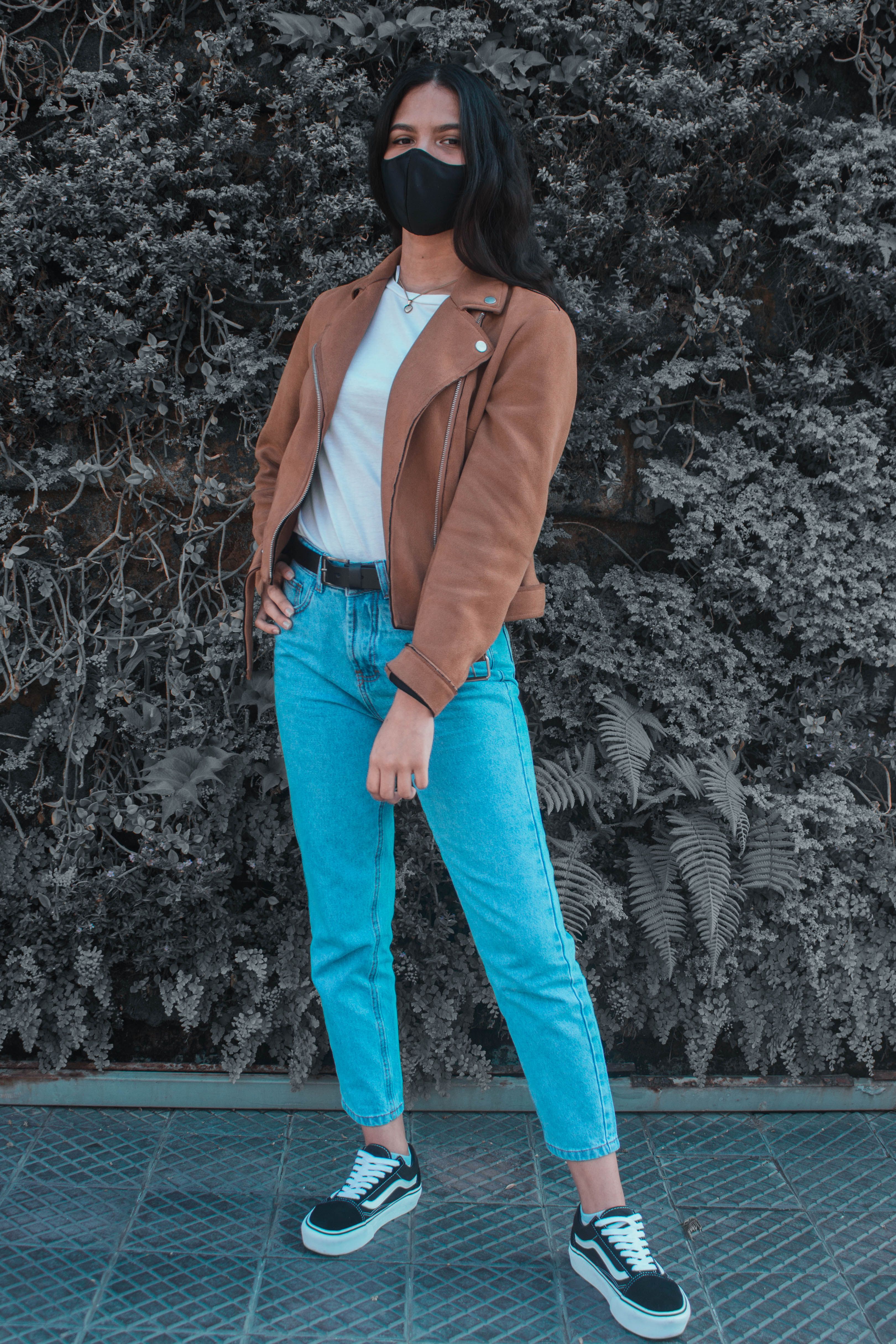 A Woman in Brown Jacket and Denim Jeans Wearing a Black Face Mask ...