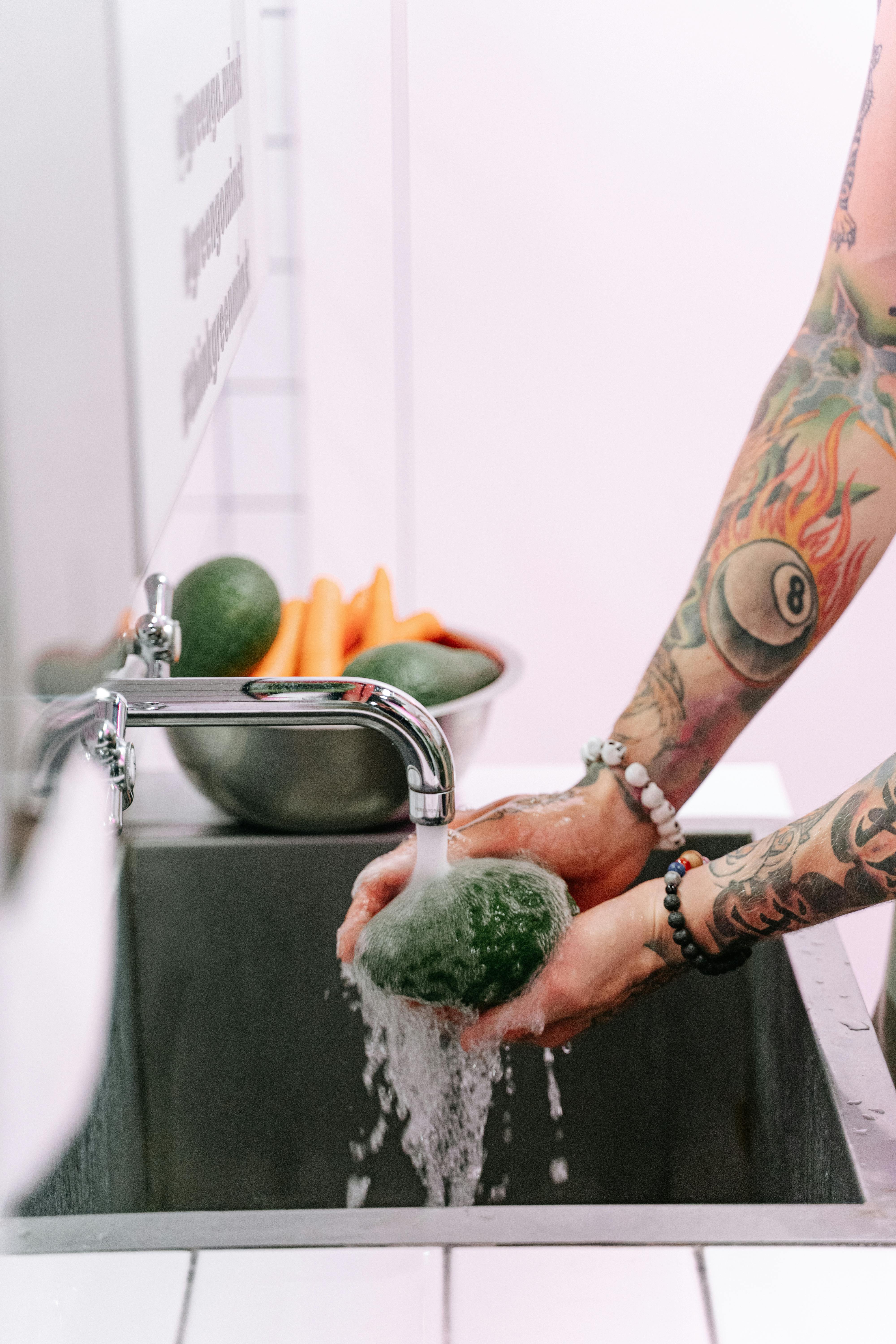 Tattooed Person washing Avocados on a Sink · Free Stock Photo