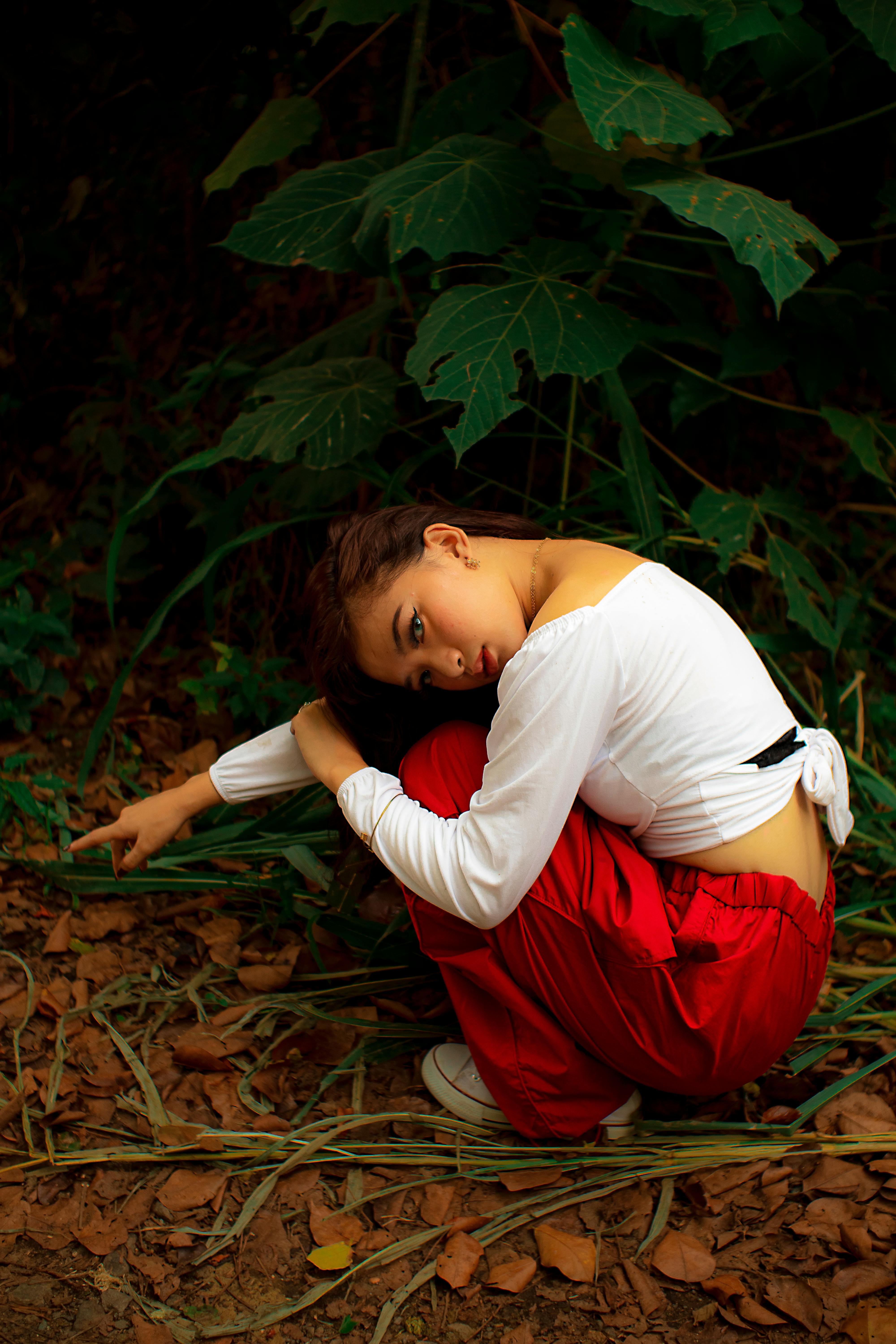 Melancholic young woman sitting on haunches and looking away in forest ...