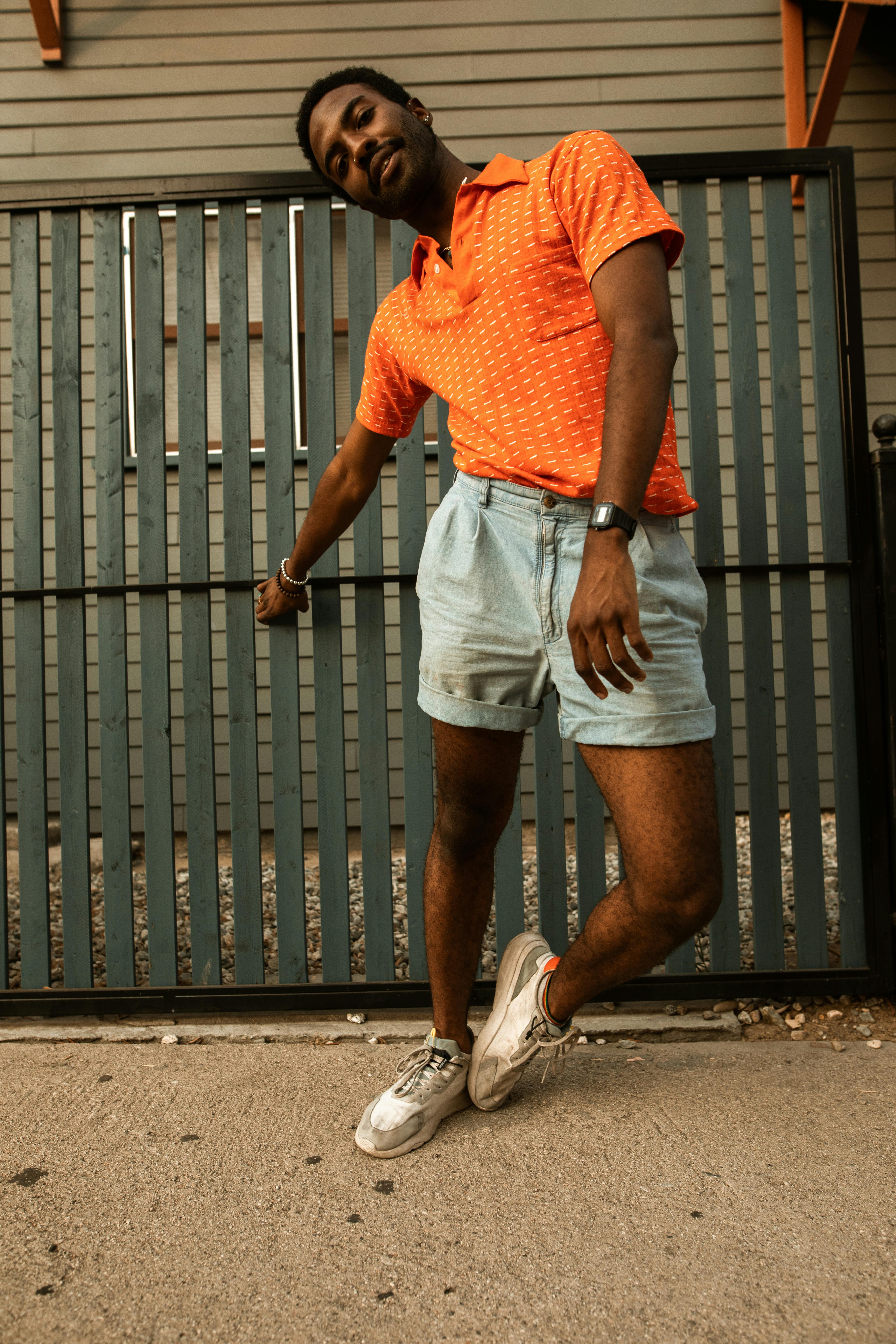 Handsome Man in Denim Shorts Posing by Fence · Free Stock Photo