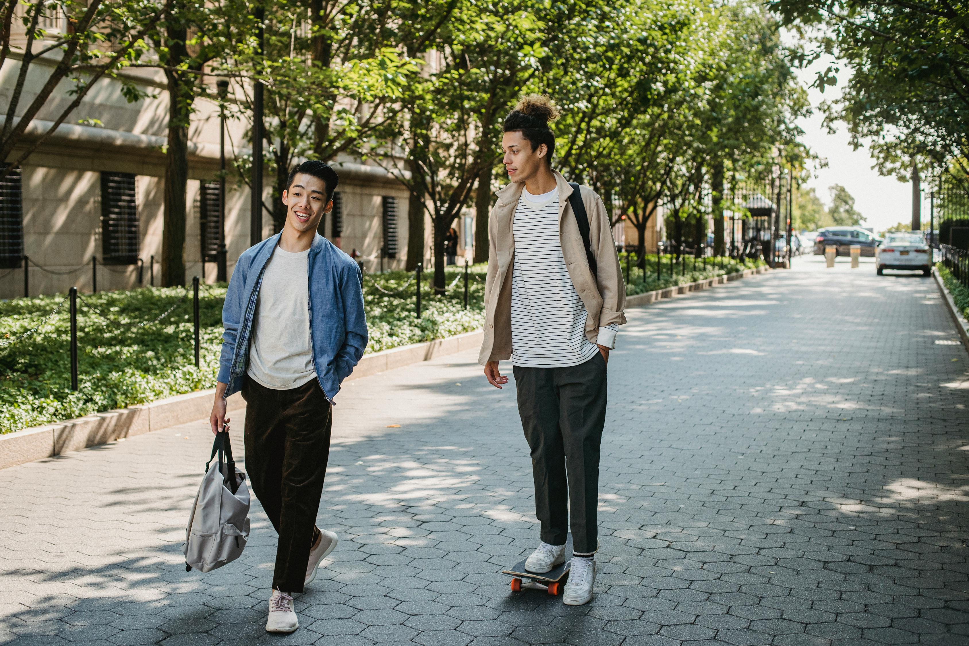 Cheerful multiethnic male friends walking on paved sidewalk together ... Cheerful multiethnic male friends walking on paved sidewalk together ...
