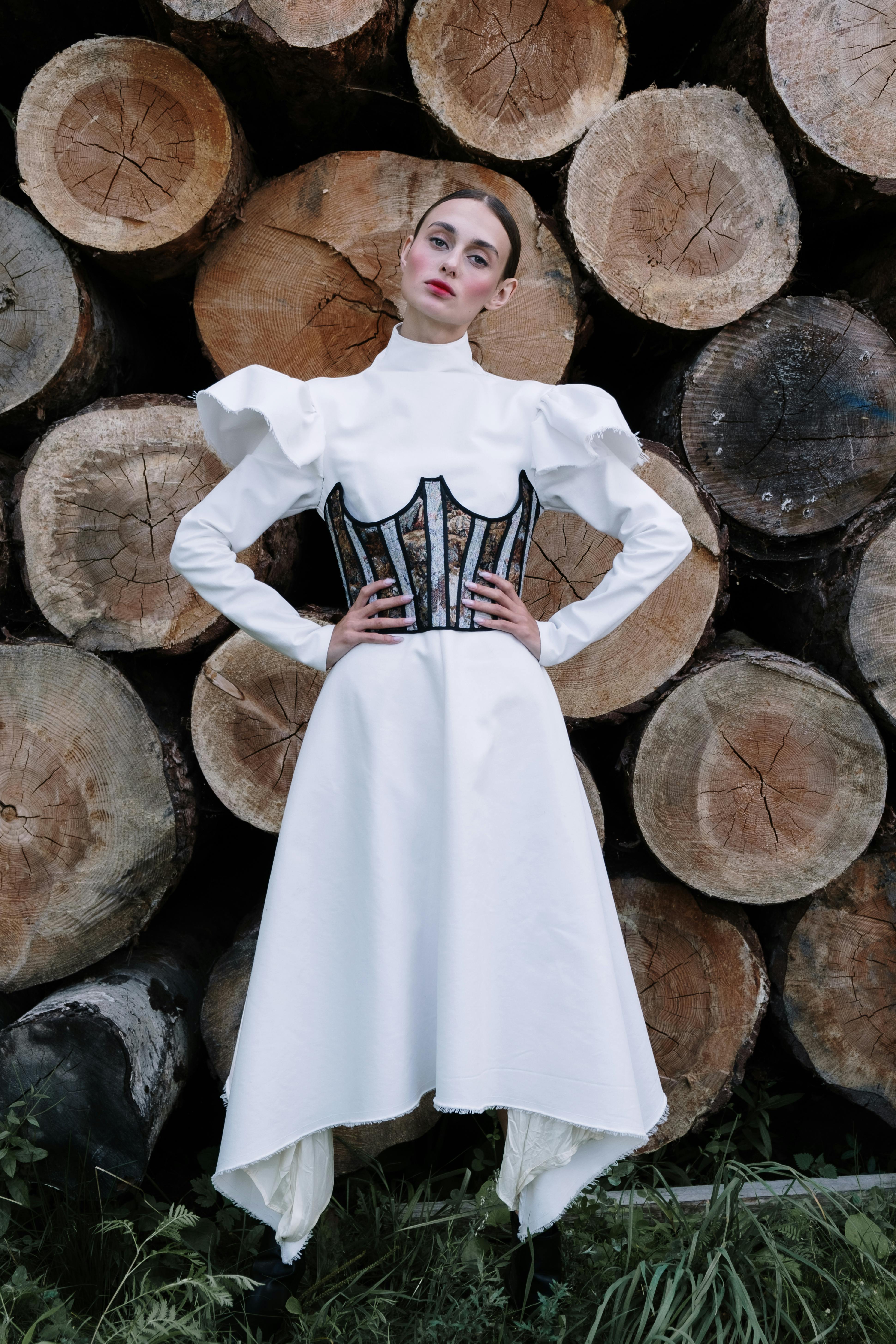 Woman in White Long Sleeve Dress Standing in Front of Wooden Logs ...
