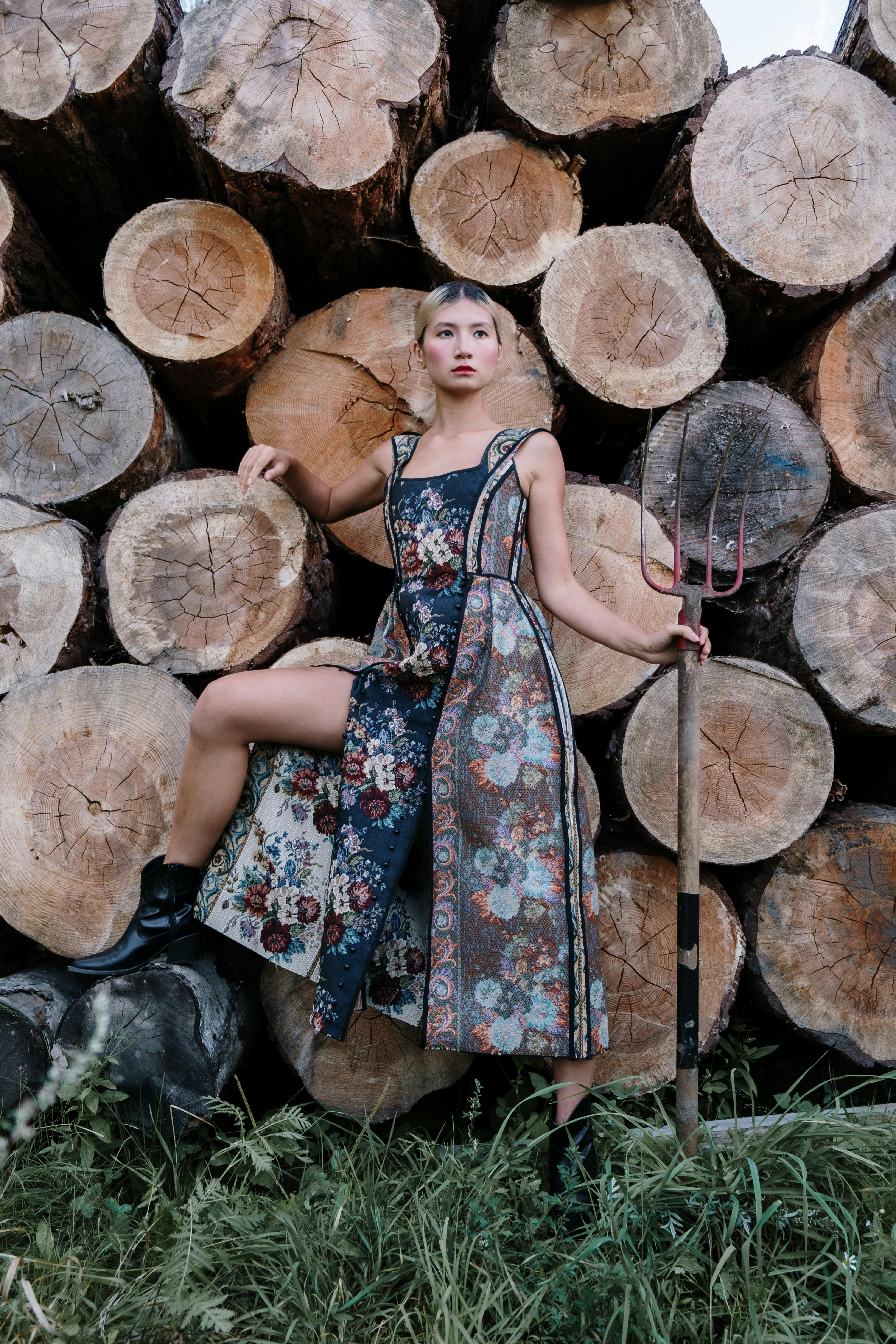 Woman in a Floral Dress Posing in Front of Wooden Logs · Free Stock Photo
