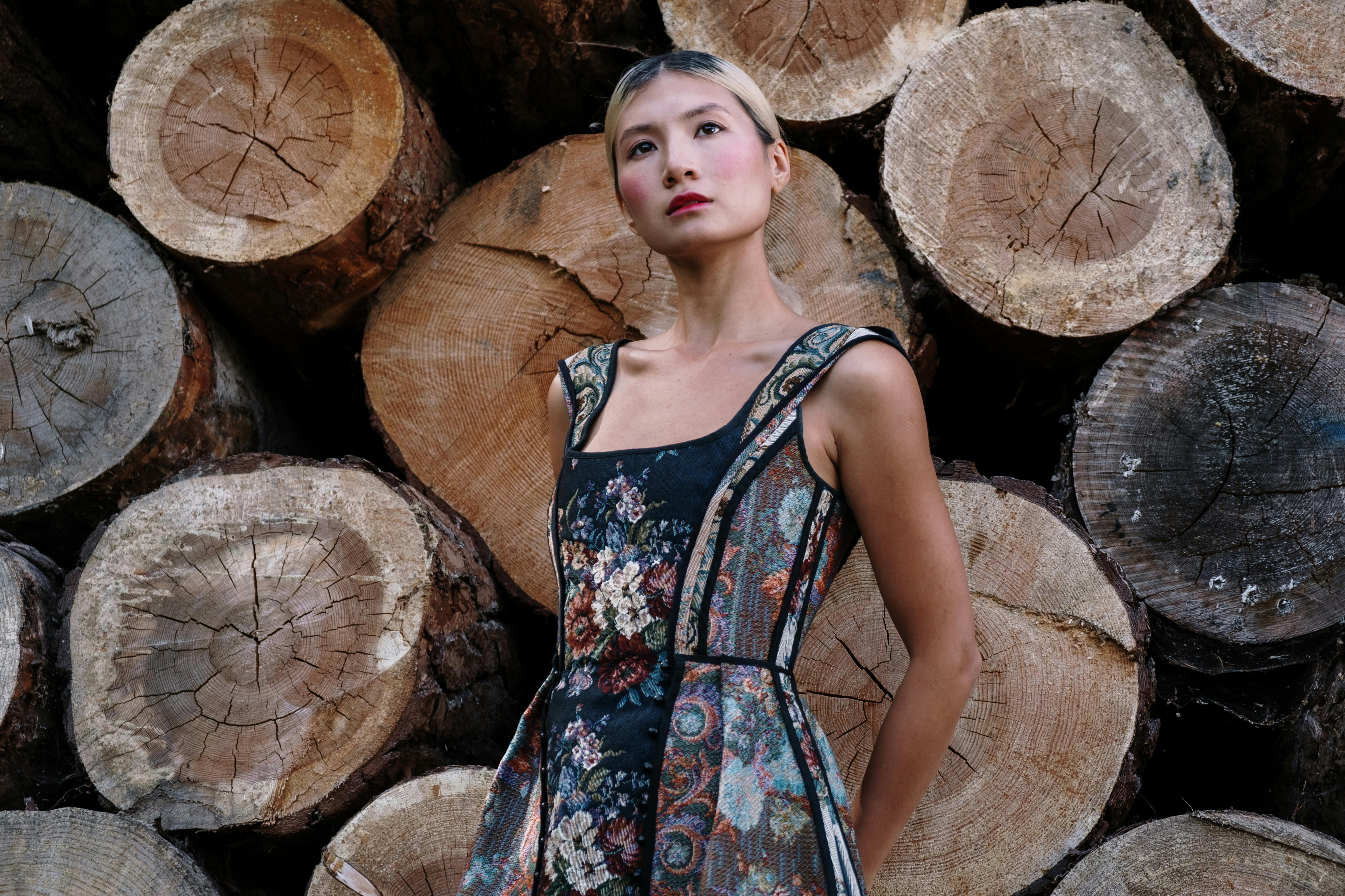 Woman in Floral Dress Standing in Front of Wooden Logs · Free Stock Photo