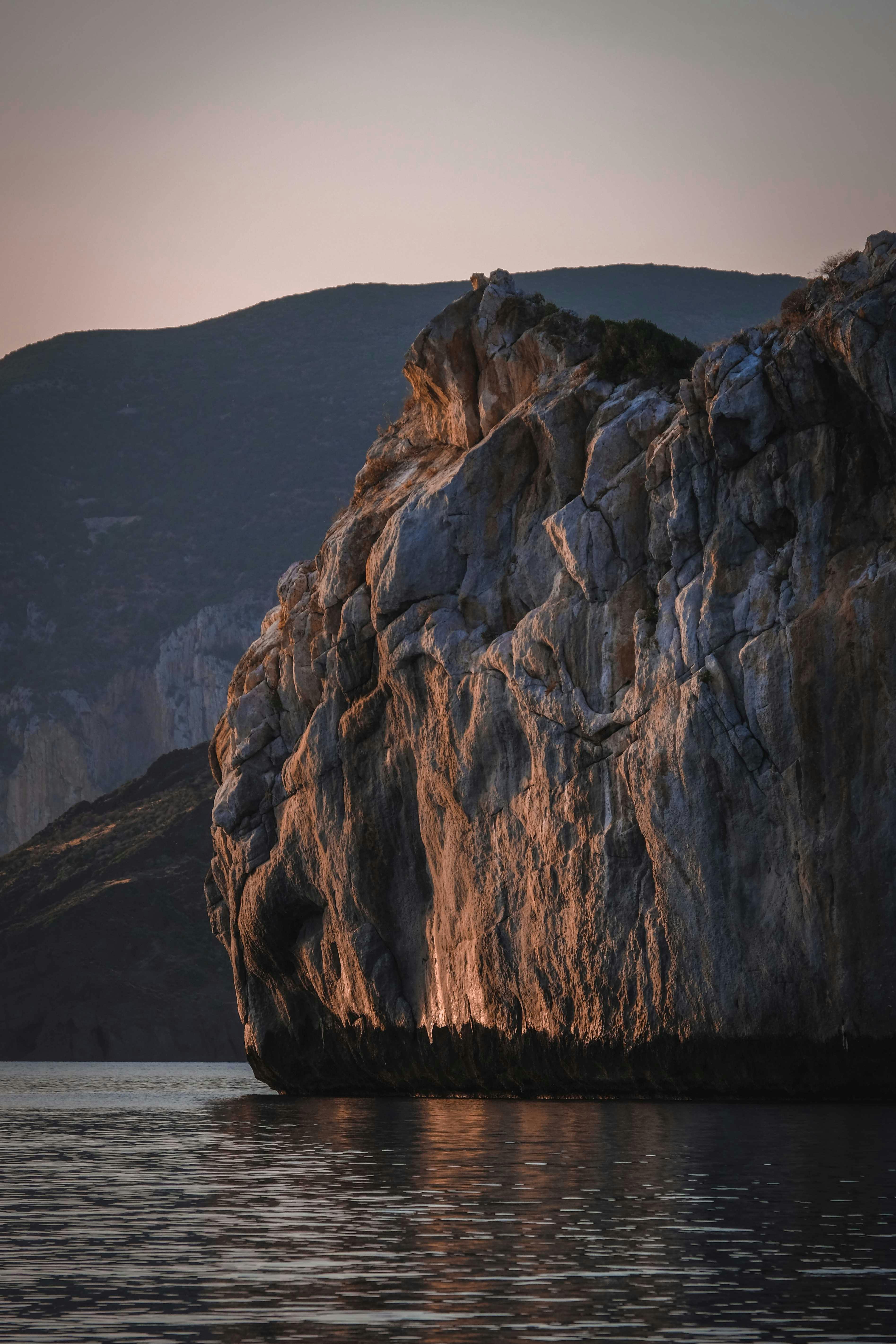 Rocky cliff in ocean water at sundown · Free Stock Photo