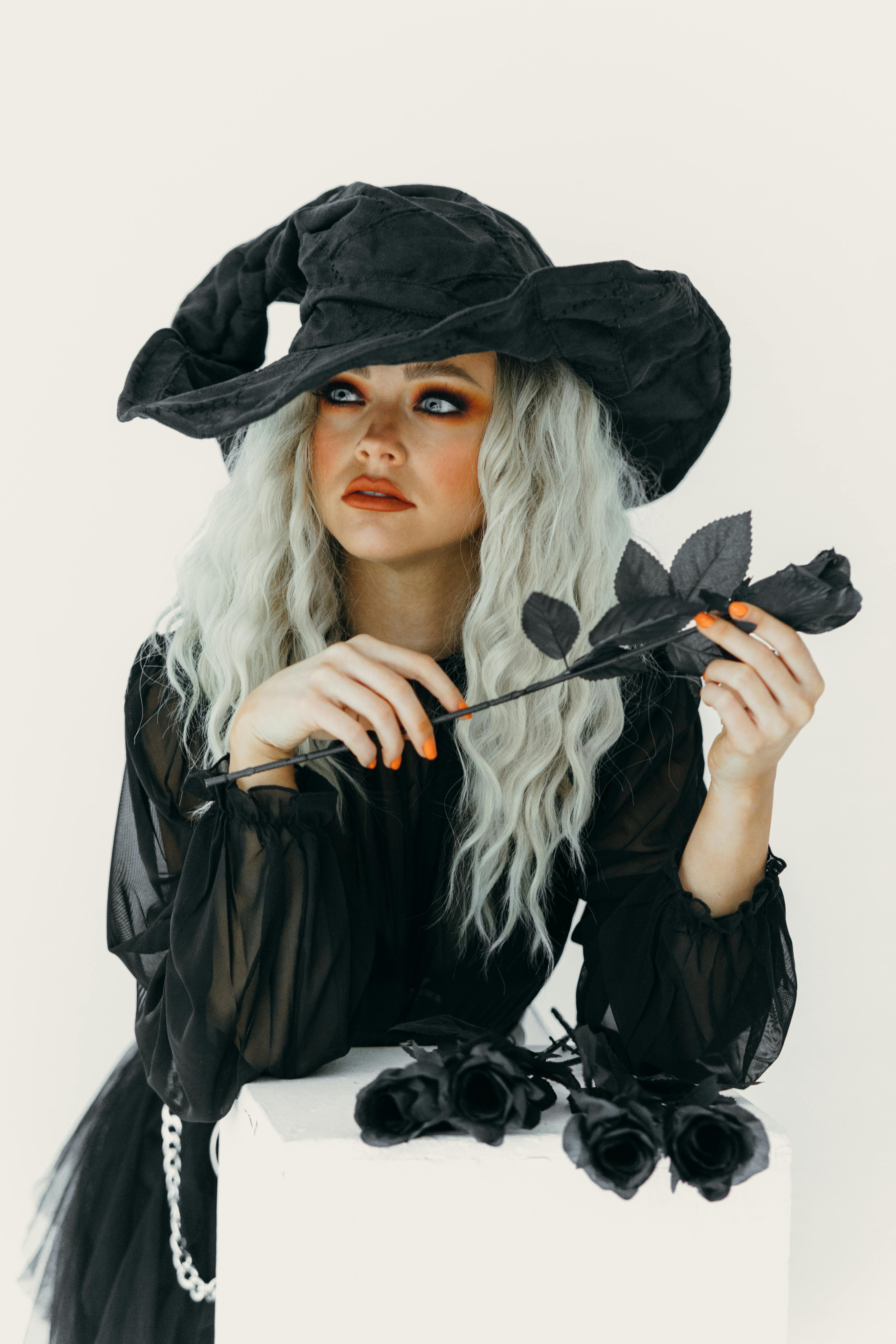 Woman in Black Witch Costume With A Book And Black Roses On Her Hands ...